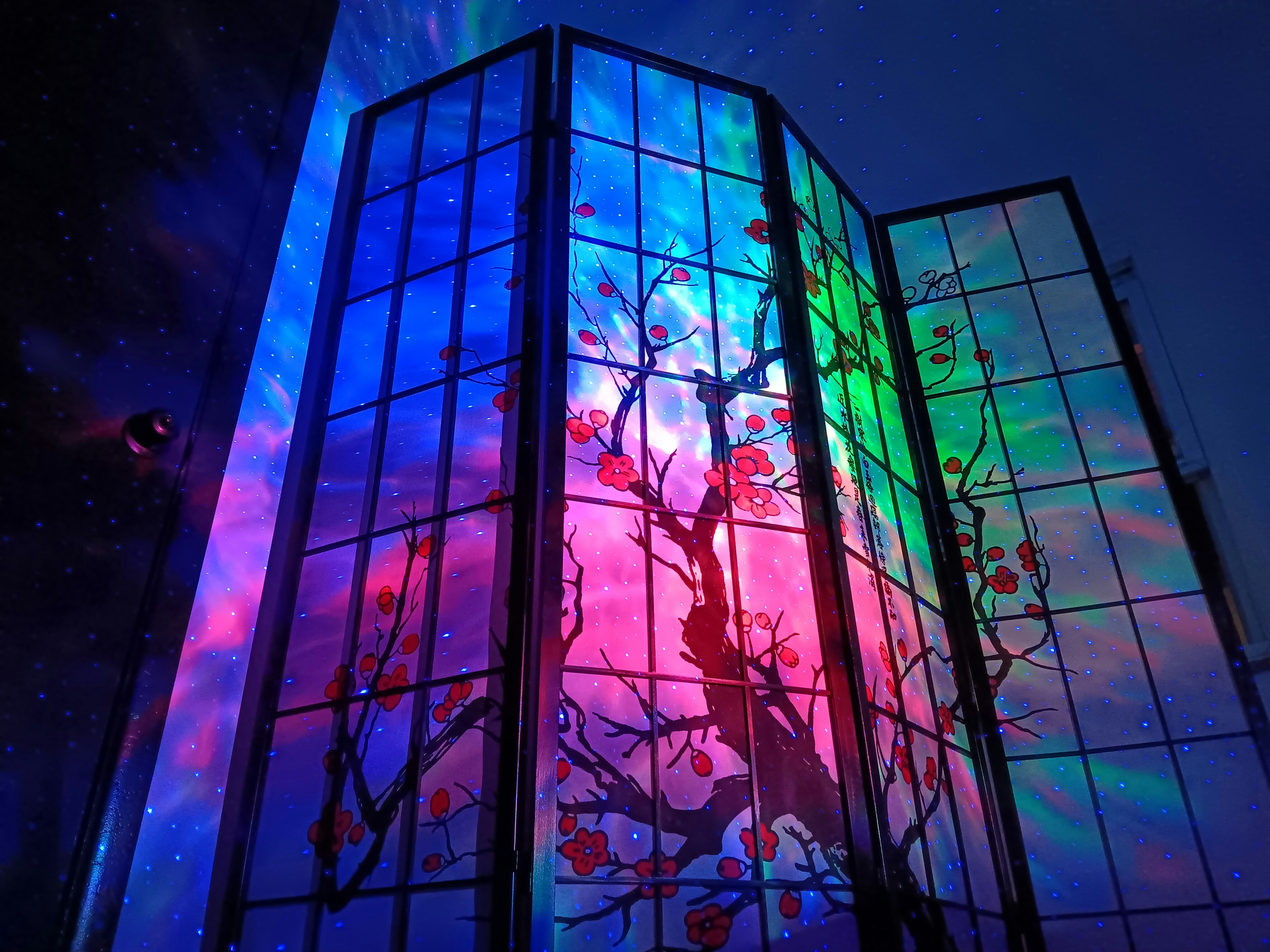 Vibrant projection of a cherry blossom tree on a glass building, illuminated with swirling colors against a twilight sky.