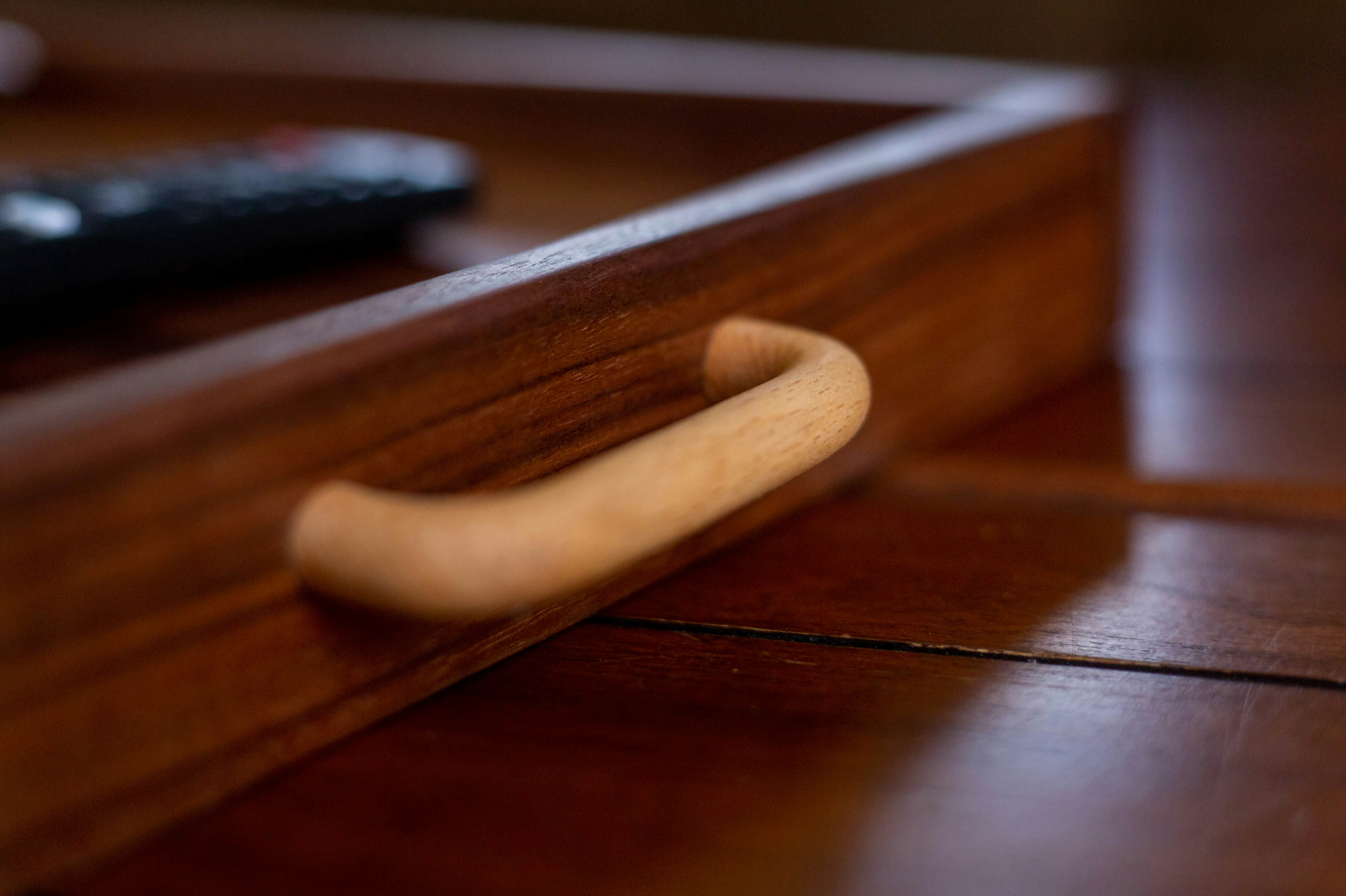 Close-up of a wooden tray handle with a remote control in the background, showcasing craftsmanship and texture.
