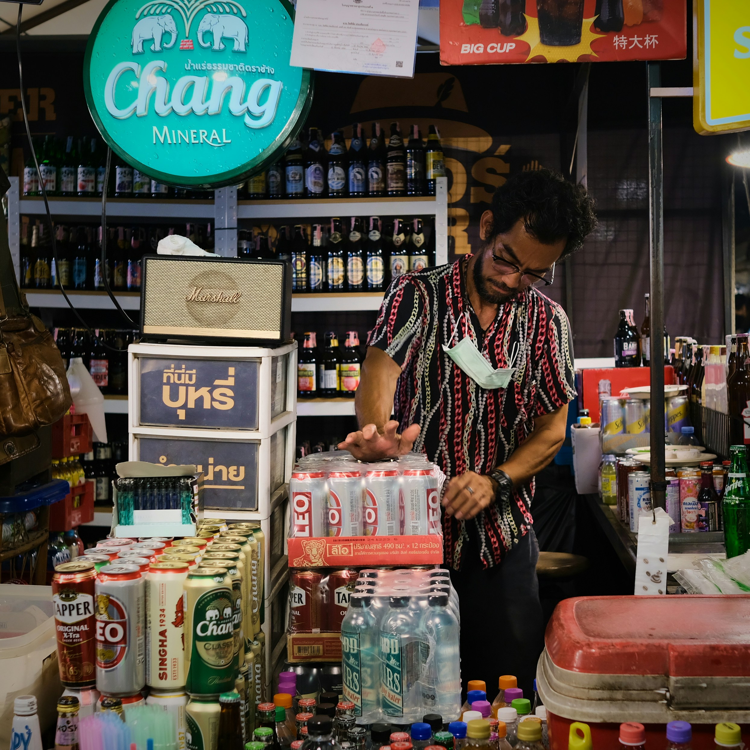 Behind the Counter: Can-Stacks and a Market Vendor Under Neon Signage