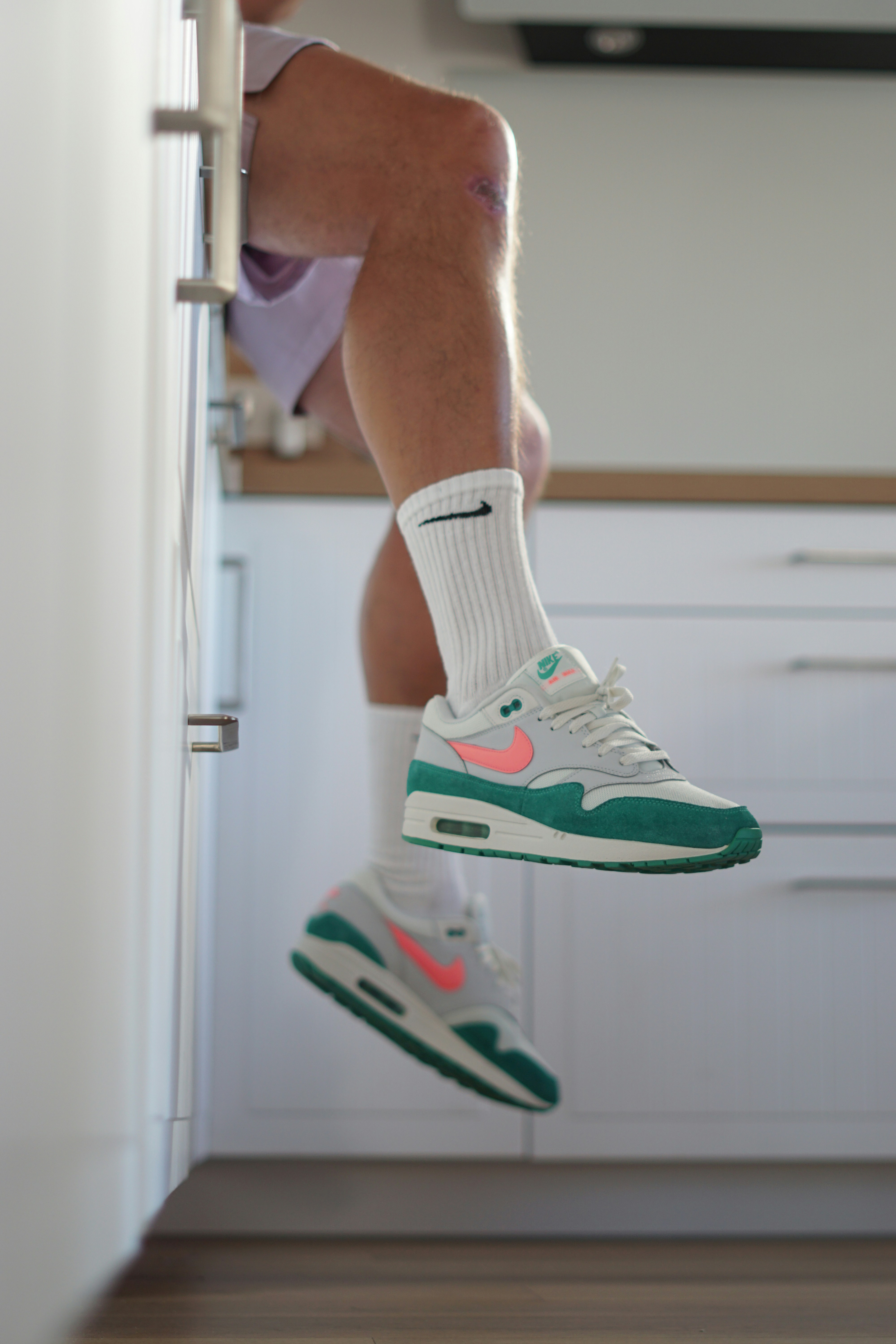 Lateral Lift: Teal-Pink Nike Sneakers Hovering Over White Cabinets