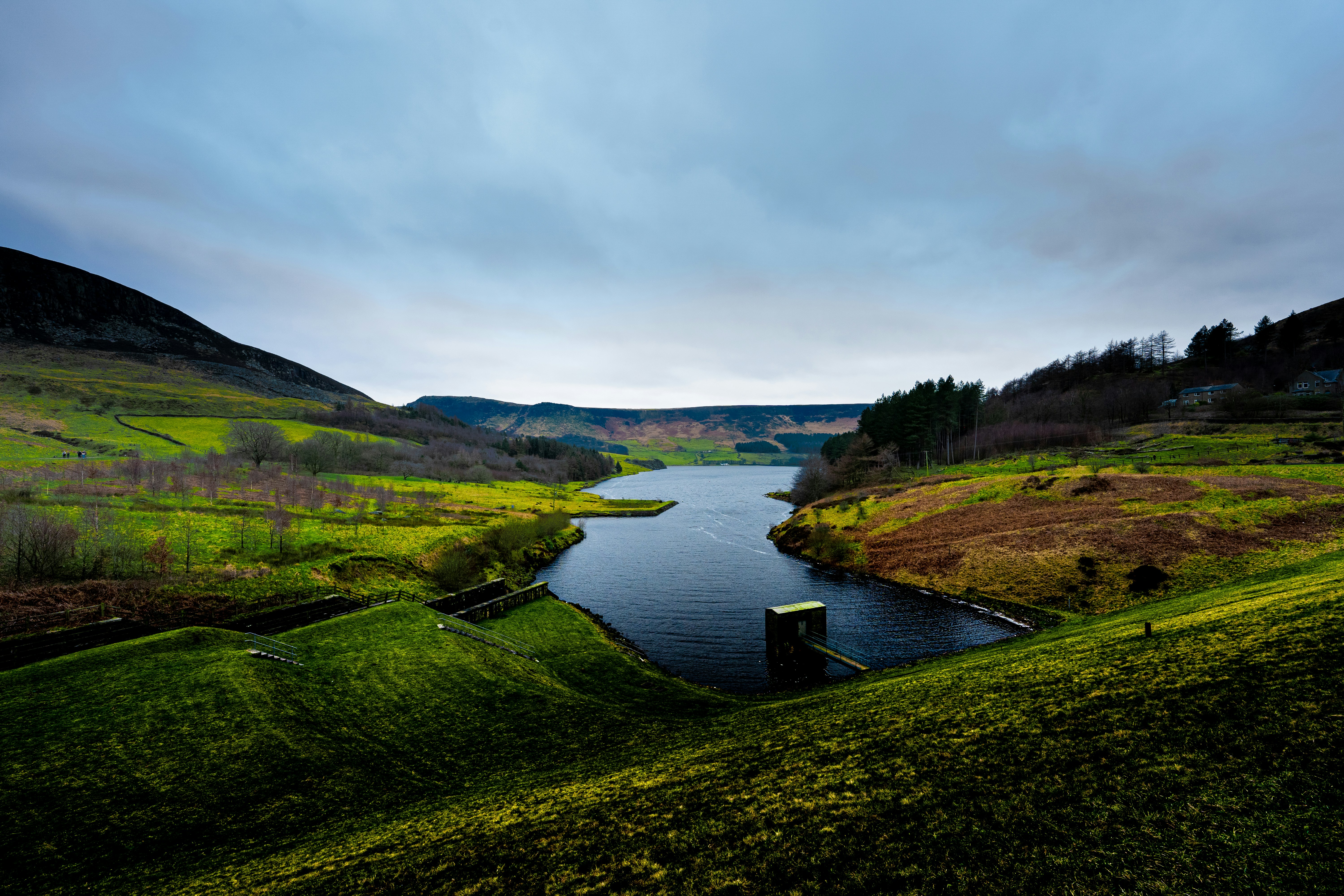 Tranquil landscape of a river winding through lush green hills under an overcast sky.