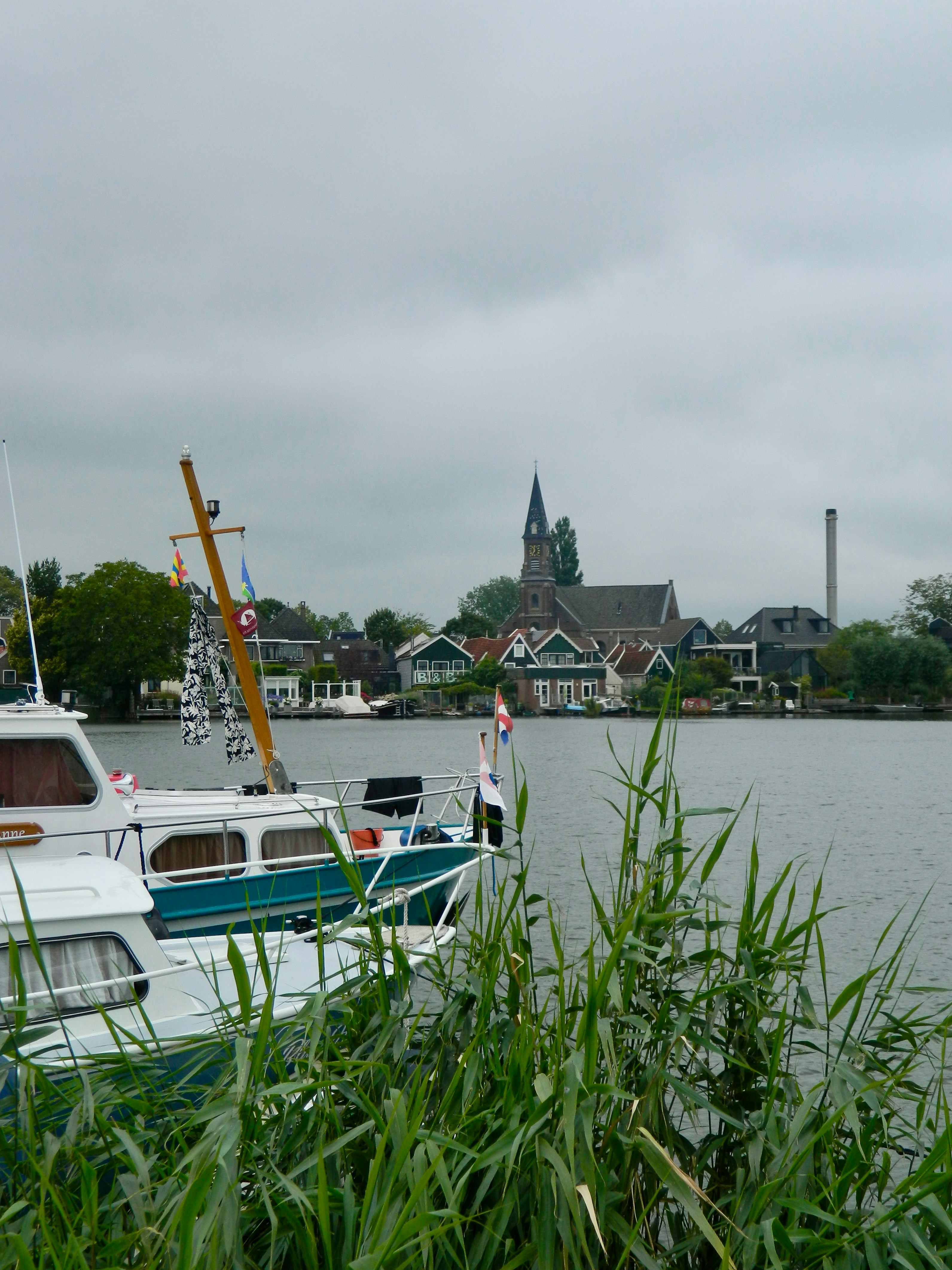 Grey Day at the Harbor: Boats, Reeds, and a Church Spire Across the Water