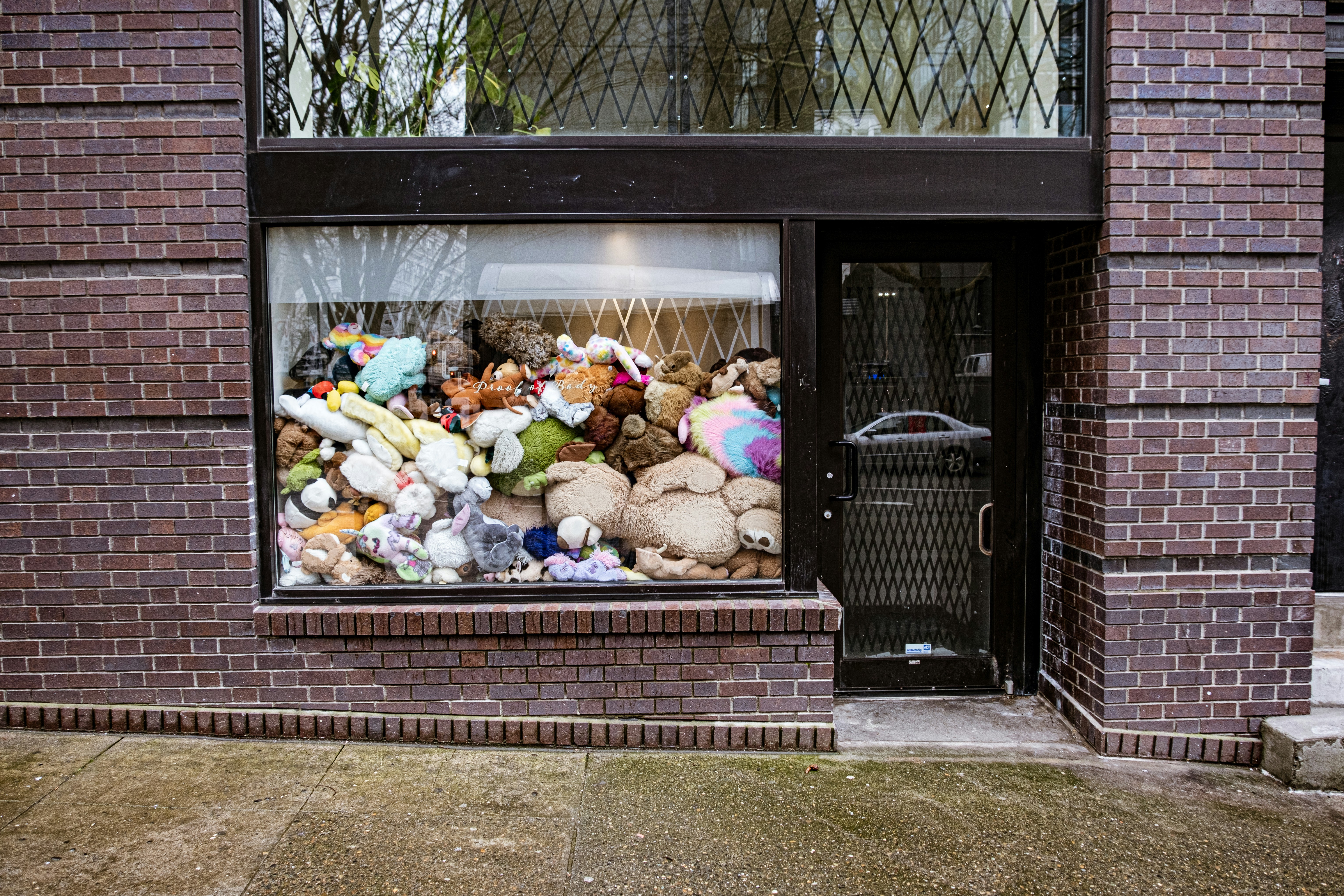 Window display overflowing with an array of plush toys, showcasing a whimsical collection in a brick storefront.