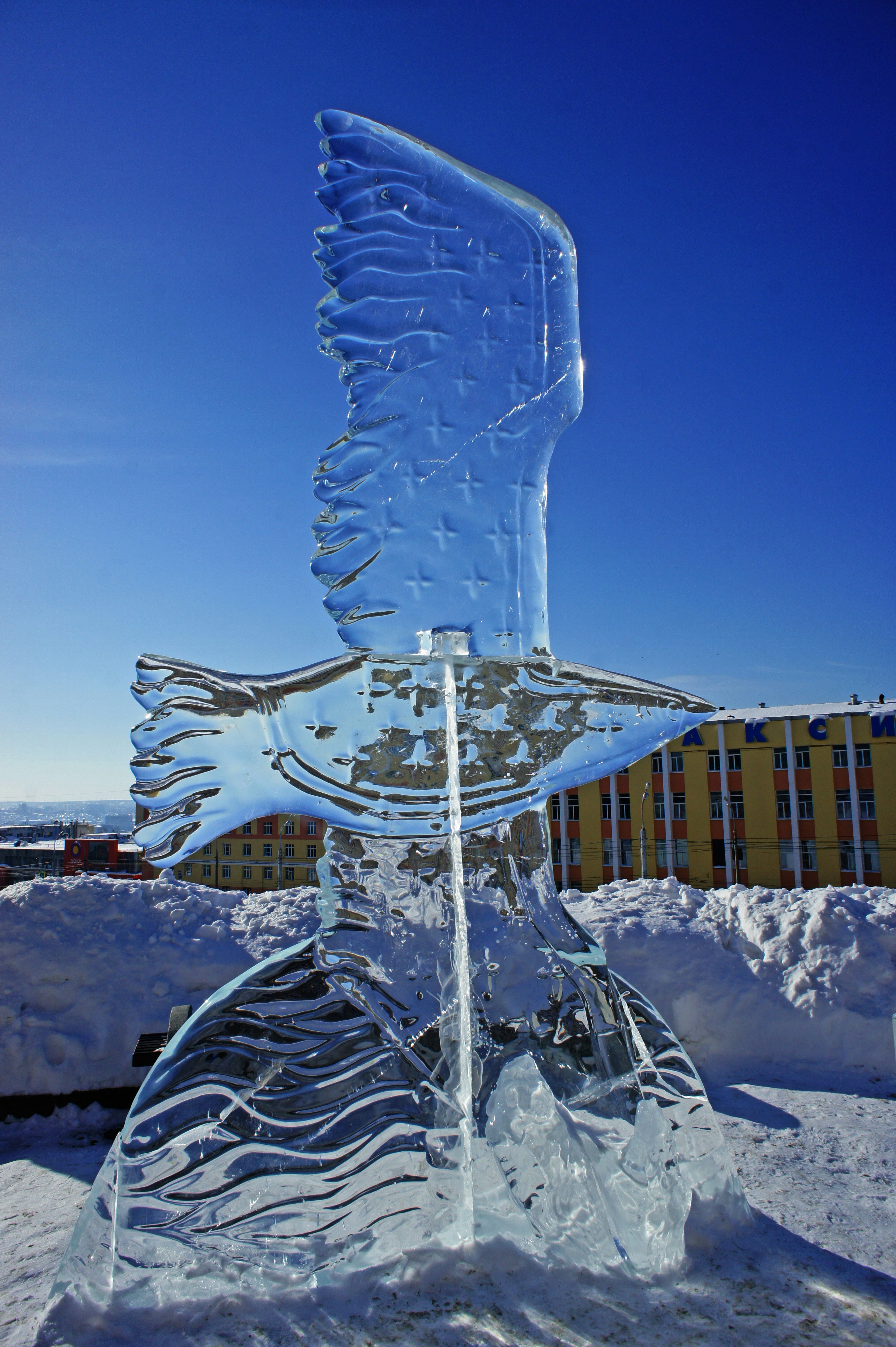 Azure Wings in Ice: A Sunlit Bird Sculpture Against Winter Blues