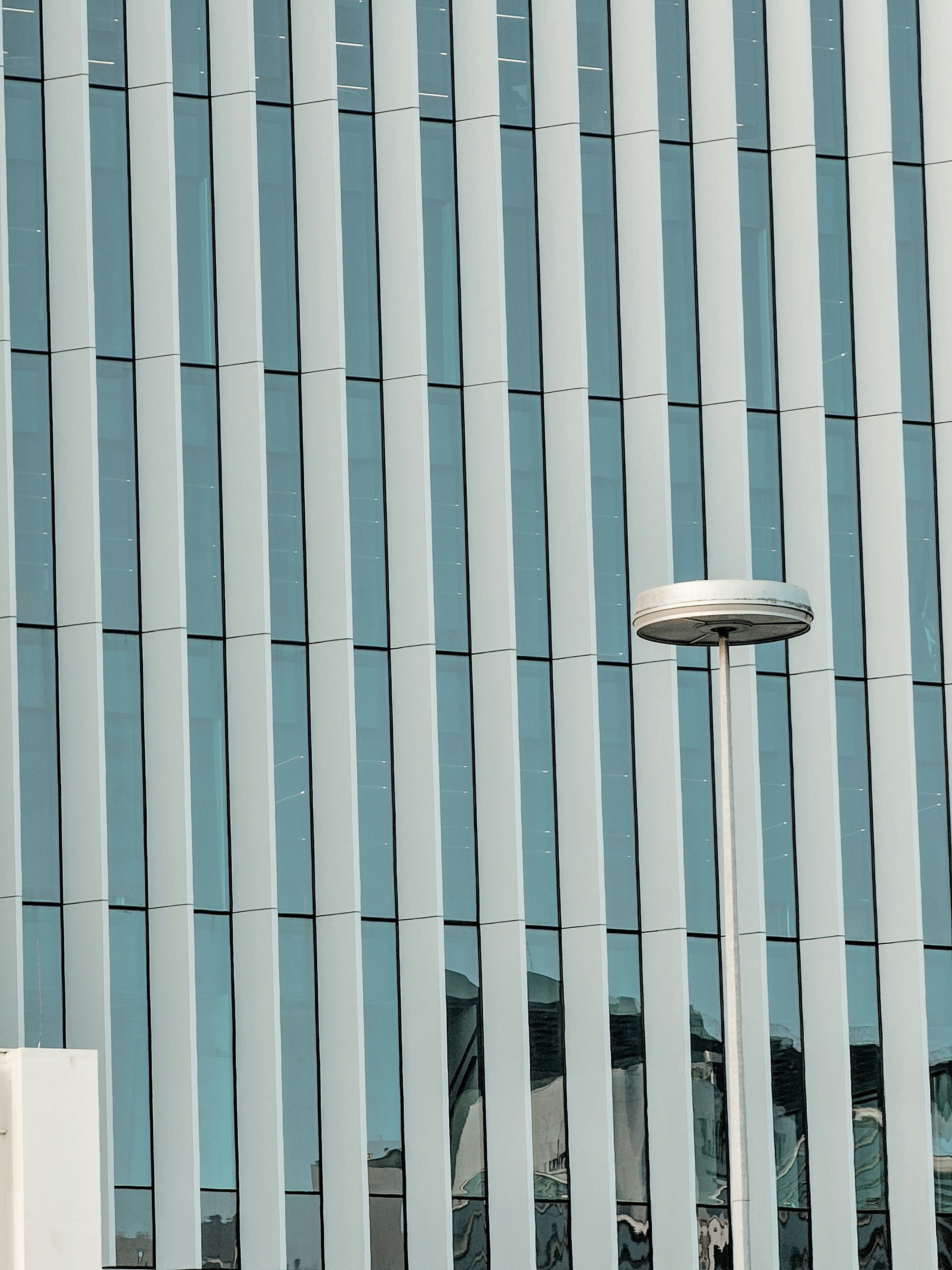 A photograph of a modern glass-clad building with vertical mullions and a lone streetlamp.