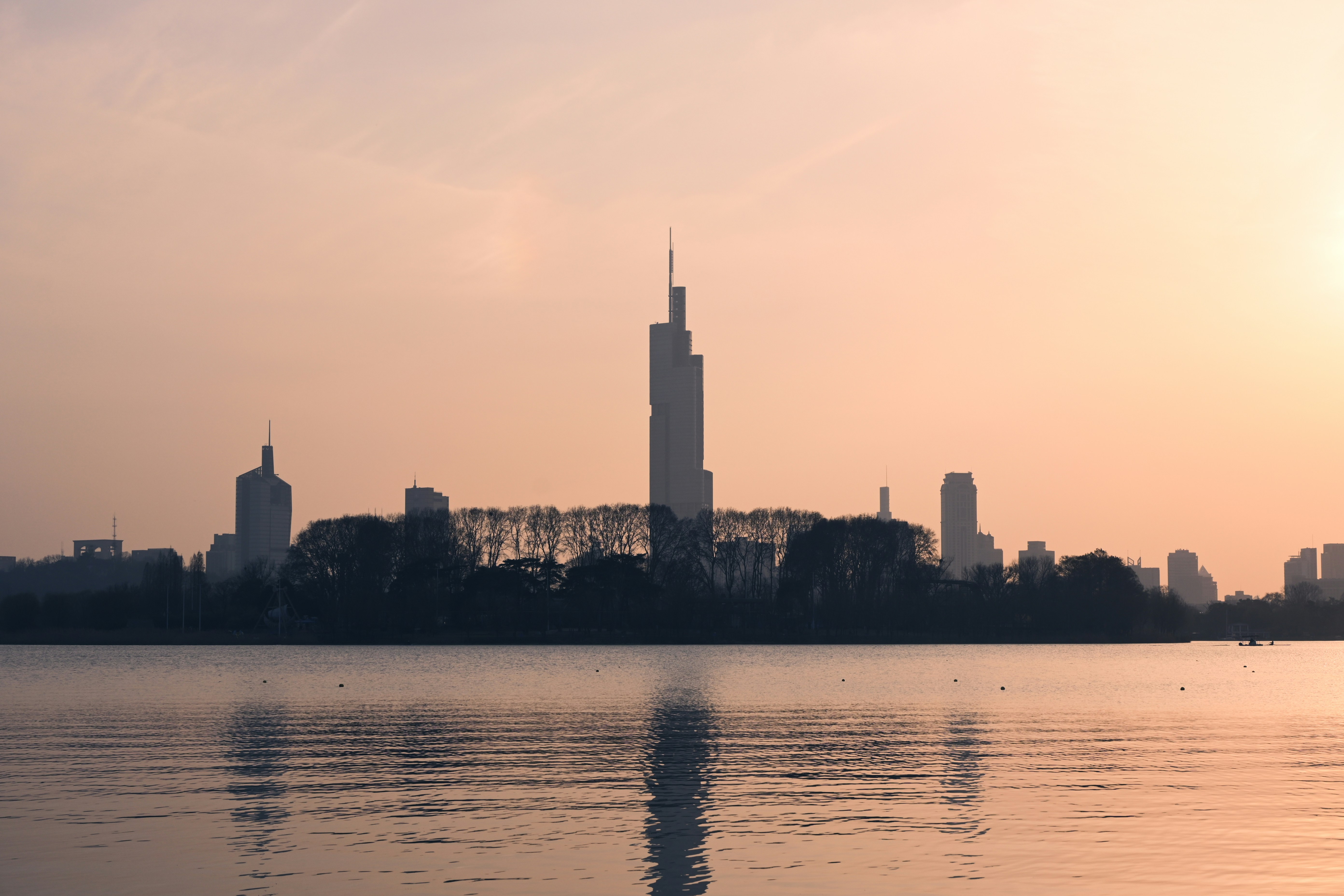 City skyline with a prominent tower at sunset, reflected in calm waters.