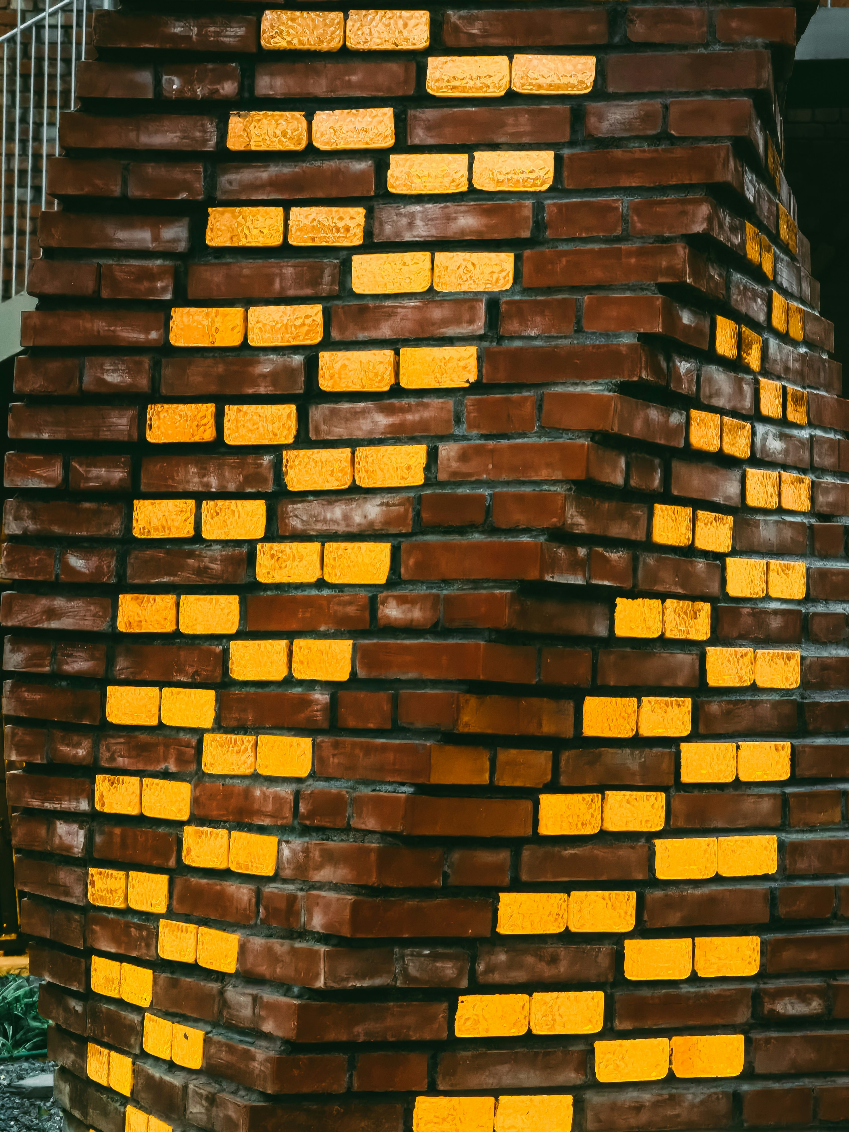Brick column with brown bricks punctuated by bright yellow blocks forming a staggered, diagonal pattern. The shot emphasizes texture and color in daylight.