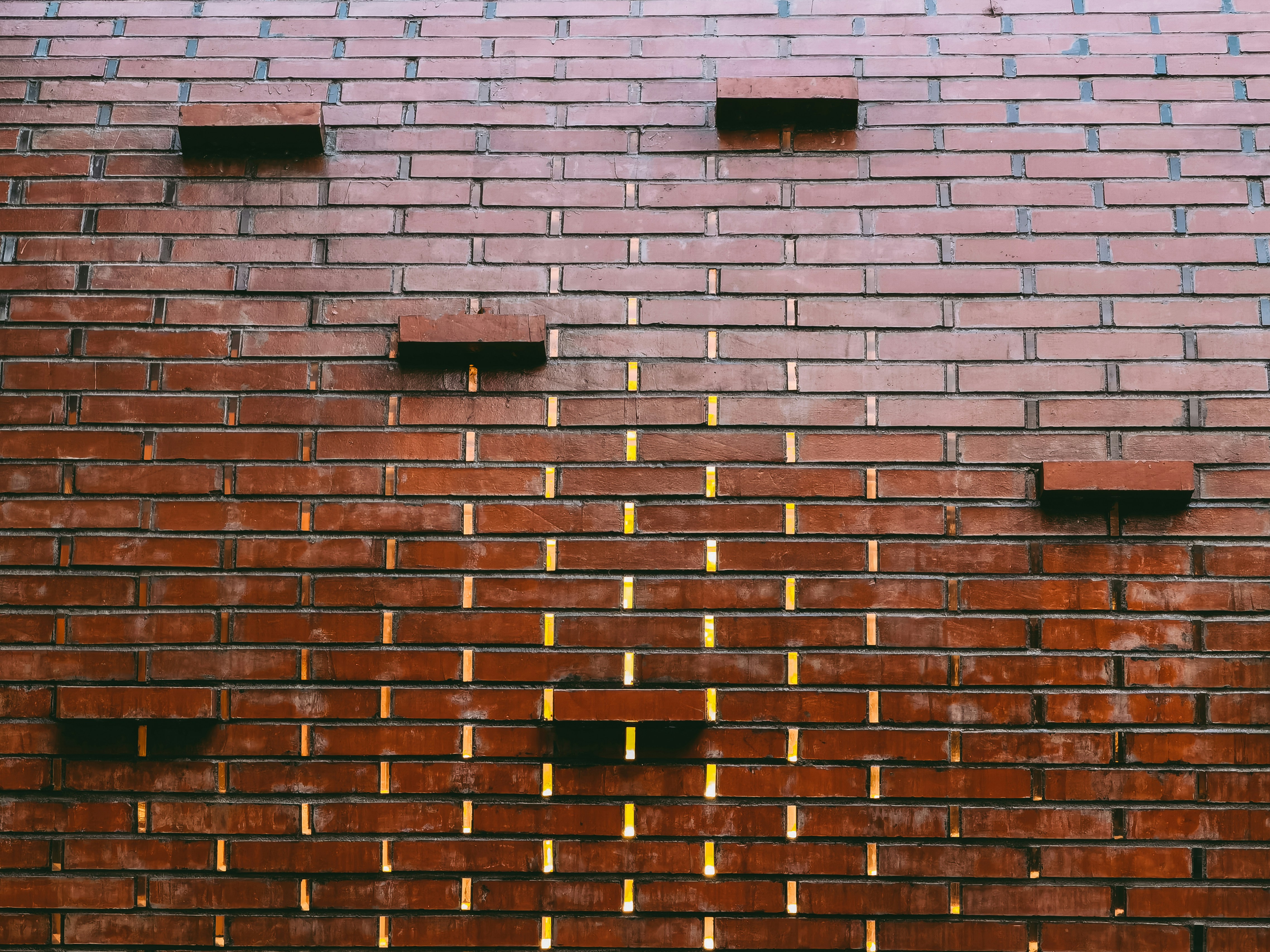 Close-up of a red brick wall with a vertical column of yellow-tinted bricks creating a bright accent. A few rectangular gaps and protruding bricks add subtle texture.