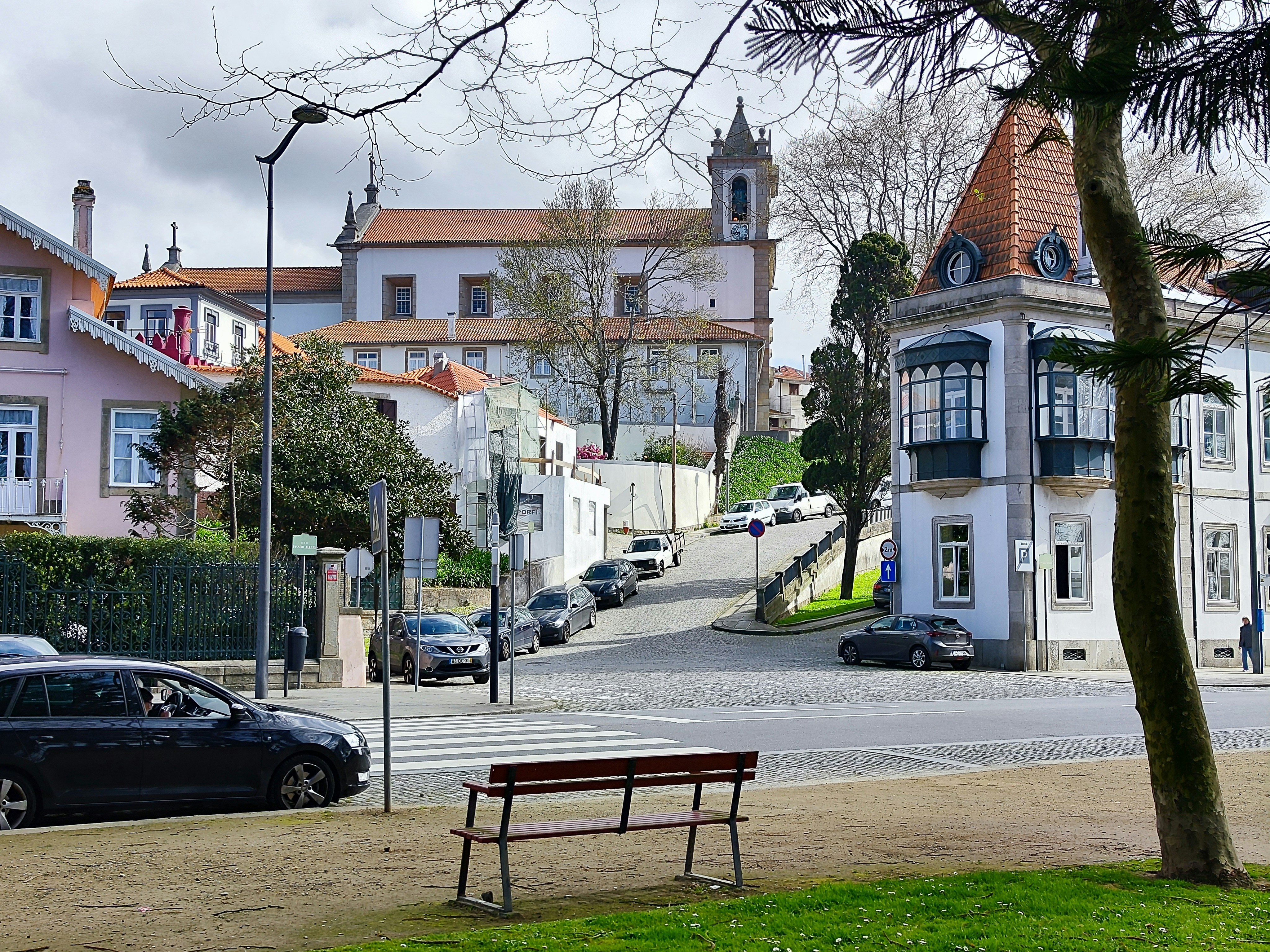 Street scene with pastel houses, a foreground bench, and a distant clocktower on a gentle hill.