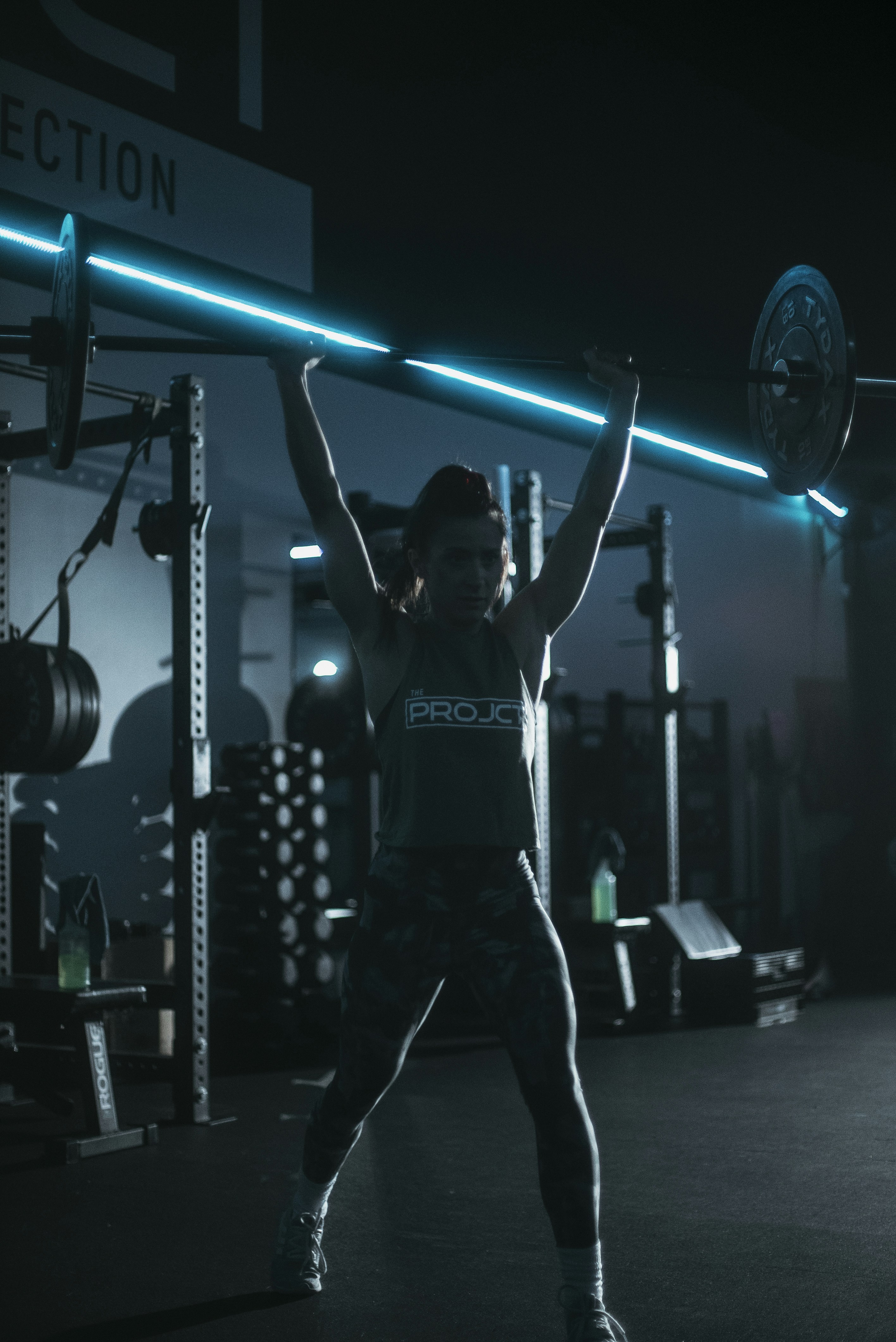 Athlete lifting a barbell illuminated by neon lights in a dimly lit gym, showcasing determination and strength.