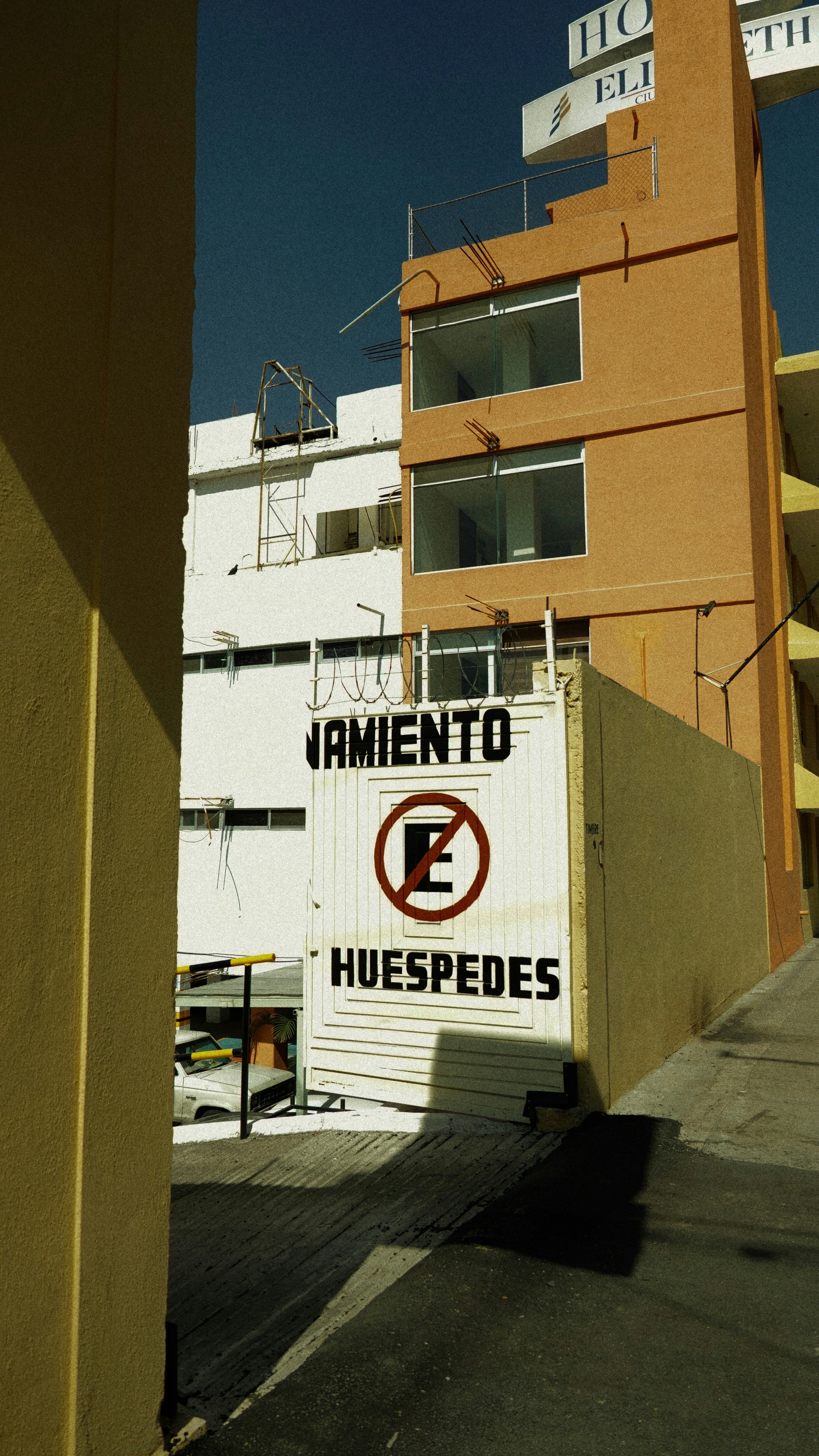 Sign indicating no guests allowed at a hotel entrance, framed by surrounding buildings. The stark contrast highlights the message.