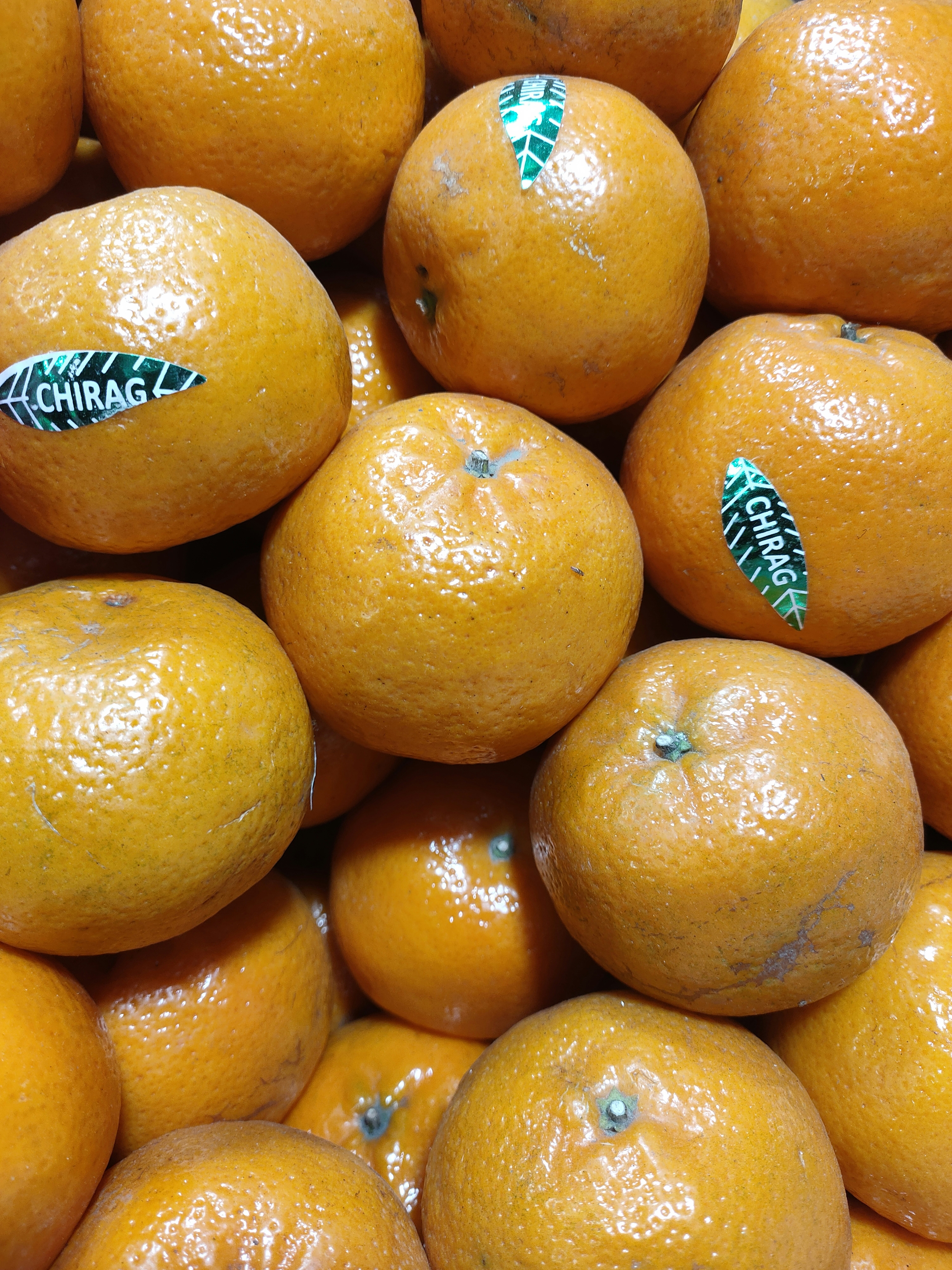 Close-up of a pile of bright oranges with glossy peels, some bearing green stickers.