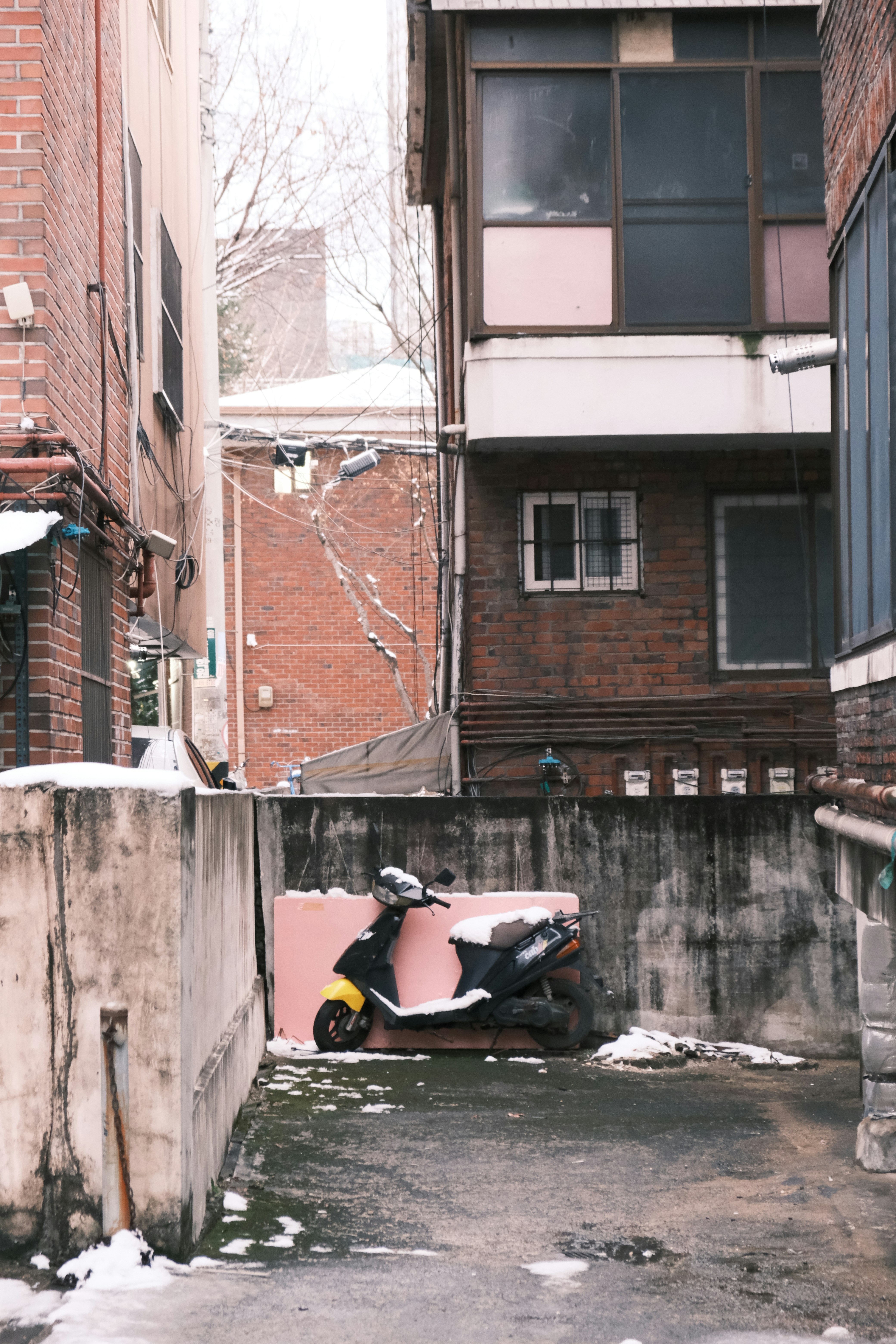 Snow-dusted scooter parked in a narrow brick alleyway during winter.