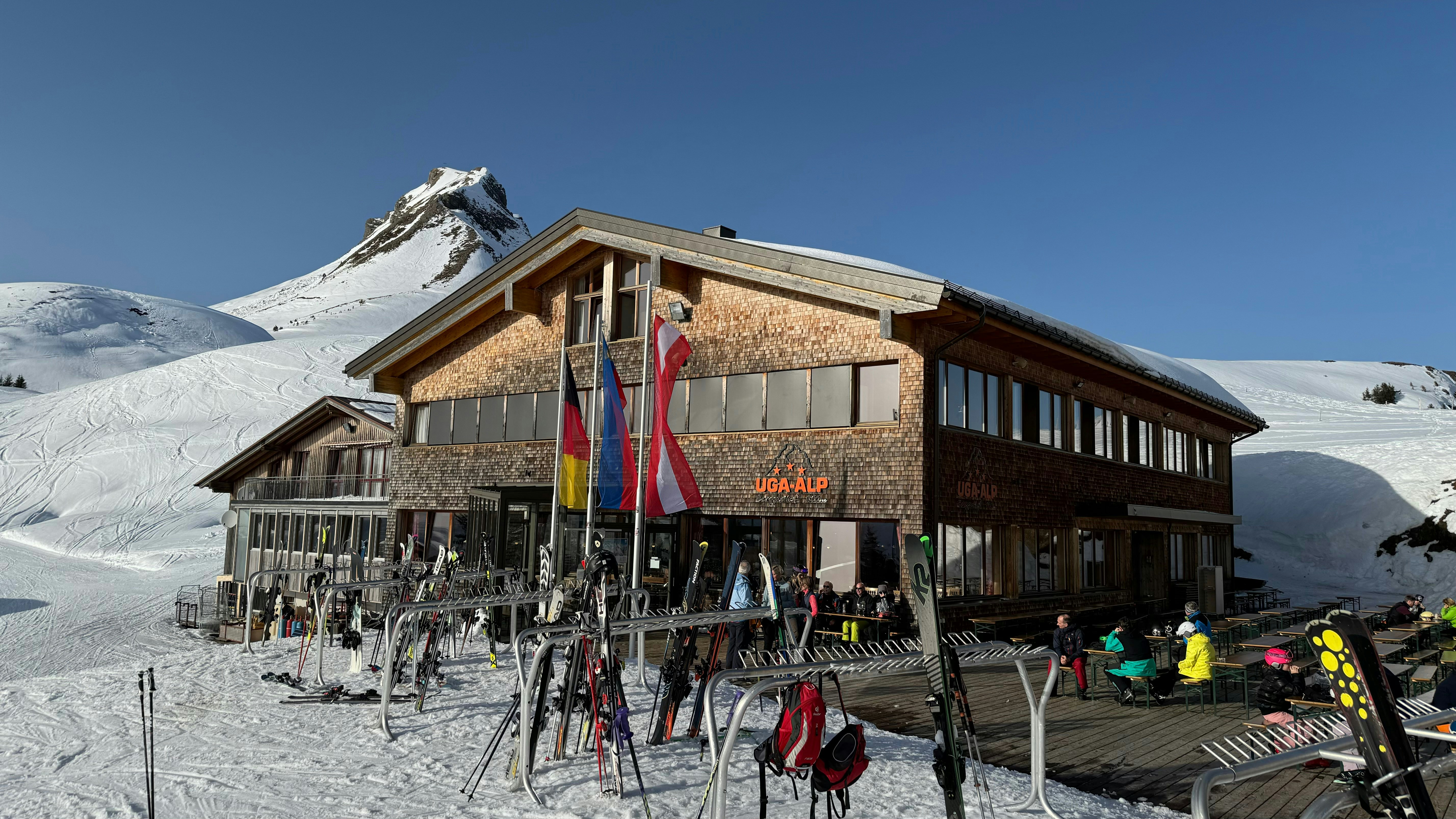 Wooden lodge surrounded by snow-covered peaks under a clear blue sky.