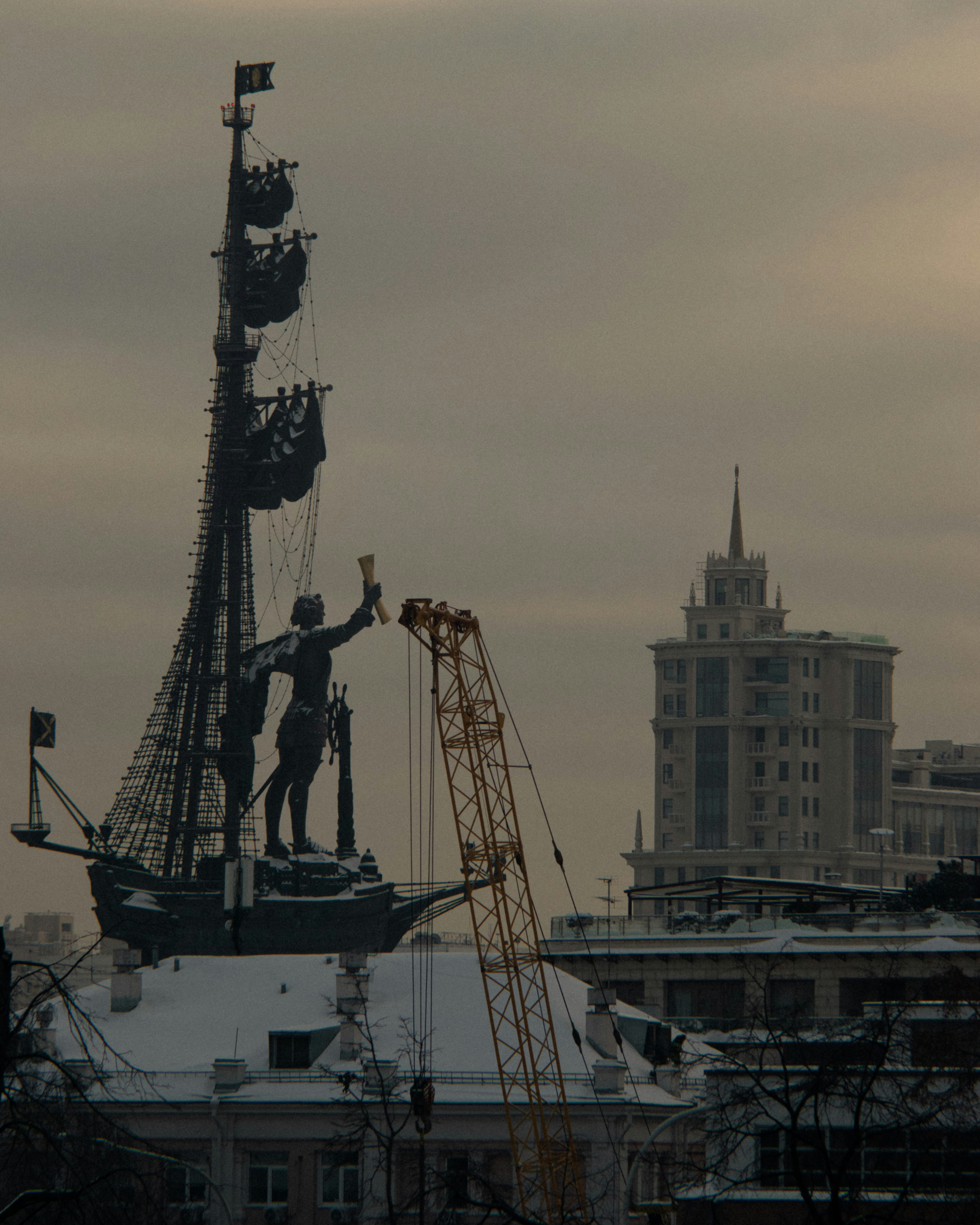 Giant Figure Rises: A Monumental Ship Figurehead Amid Urban Glass and Crane