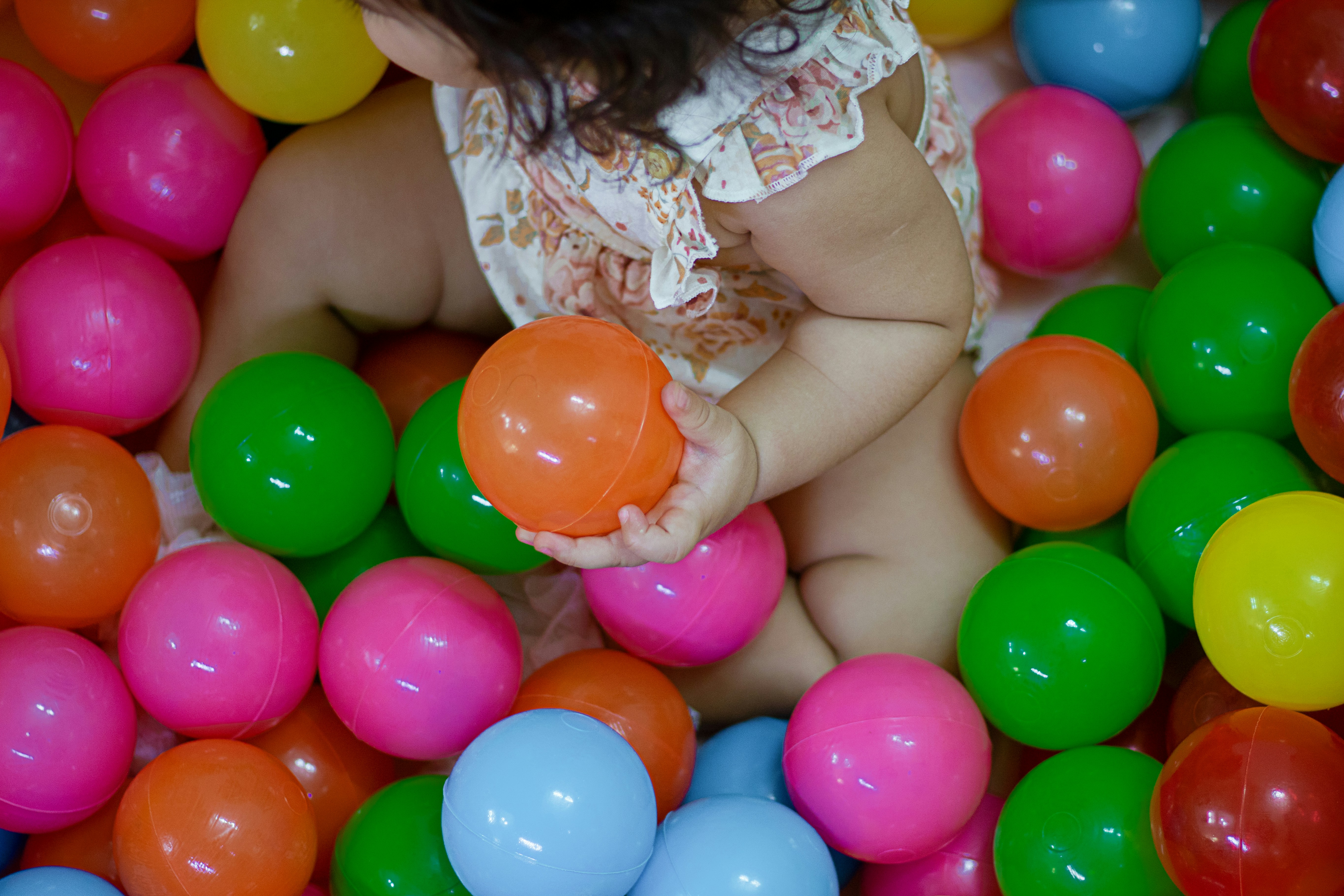 Colorful Ball Pit Moment: A Curious Child Grips an Orange Sphere