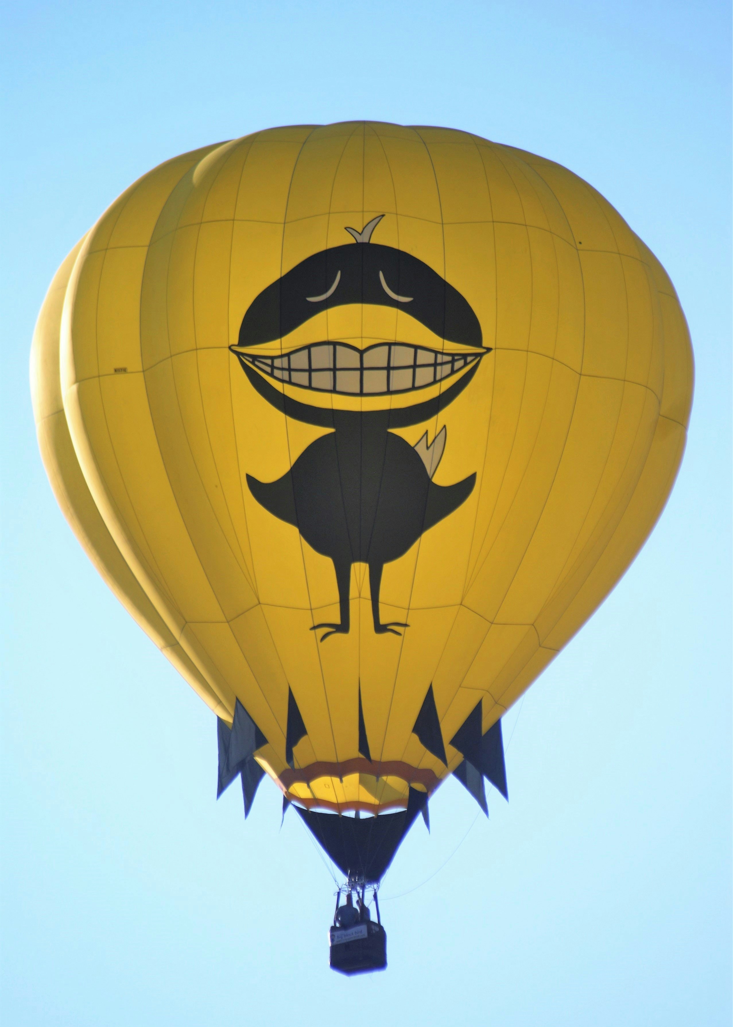 The Grinning Balloon: Yellow Mascot Soars Above a Clear Sky