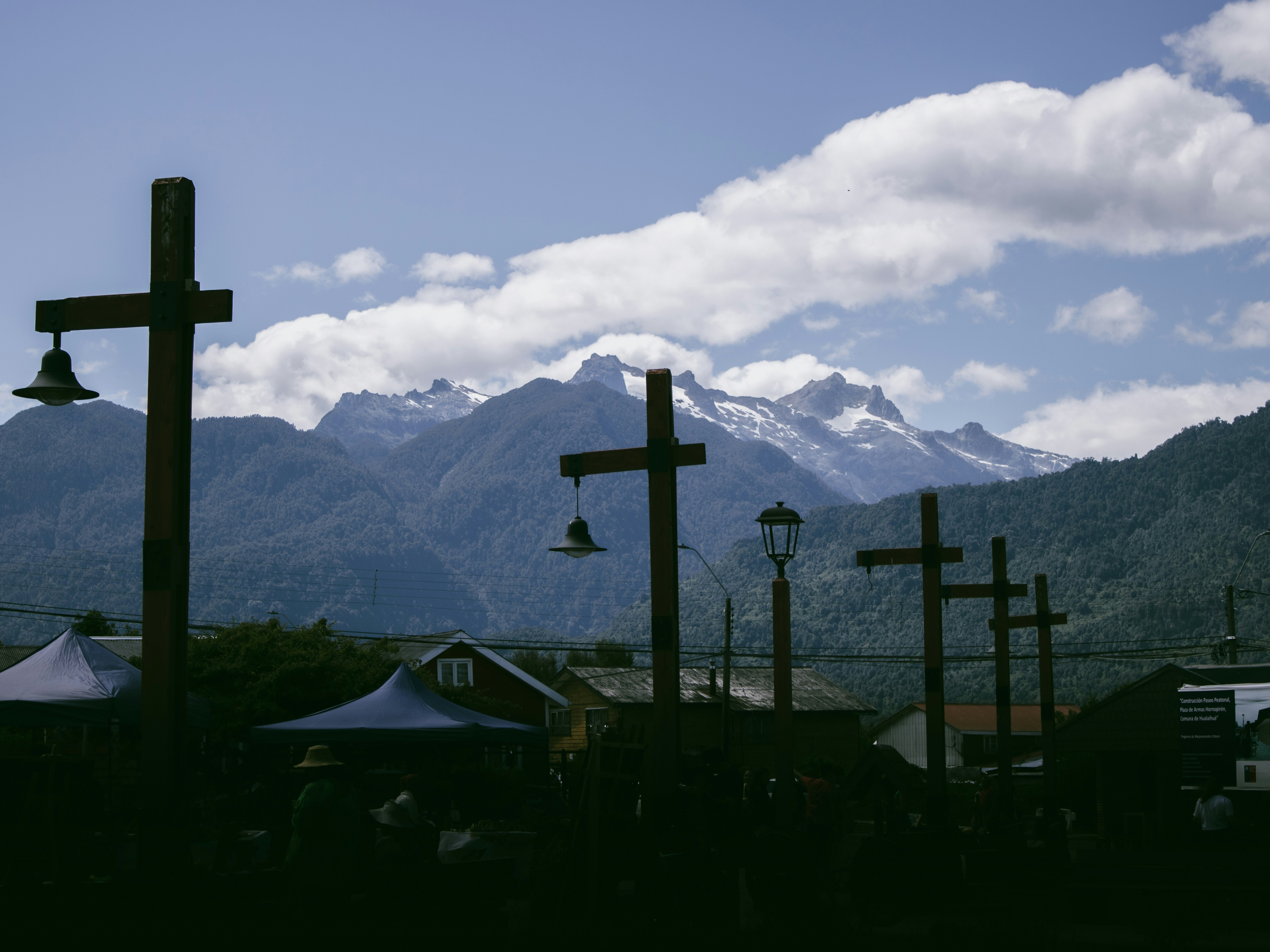 Wooden lamp posts silhouetted against snow-capped mountains under a partly cloudy sky.