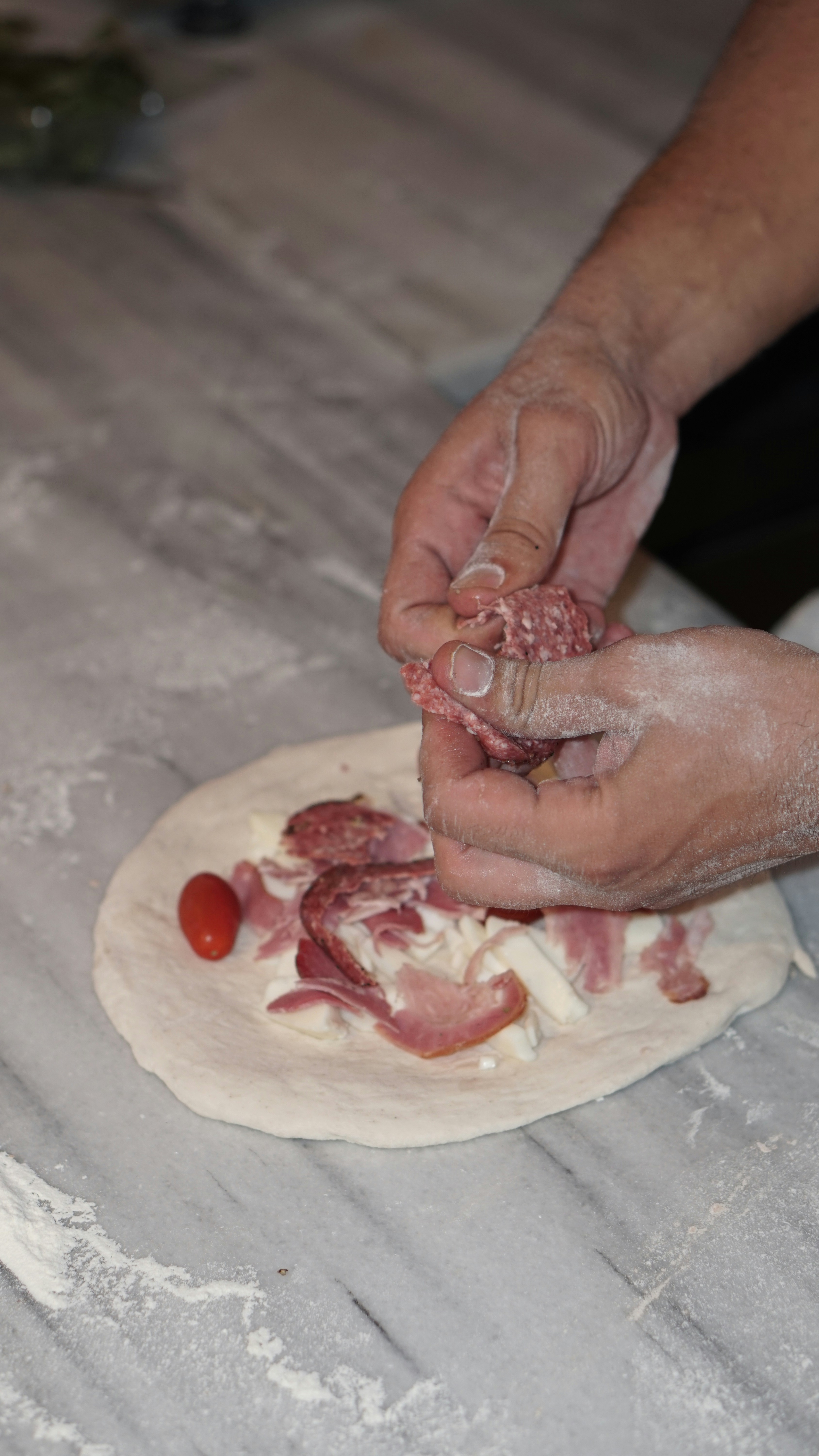 Hands shaping ground meat onto a dough circle with scattered toppings
