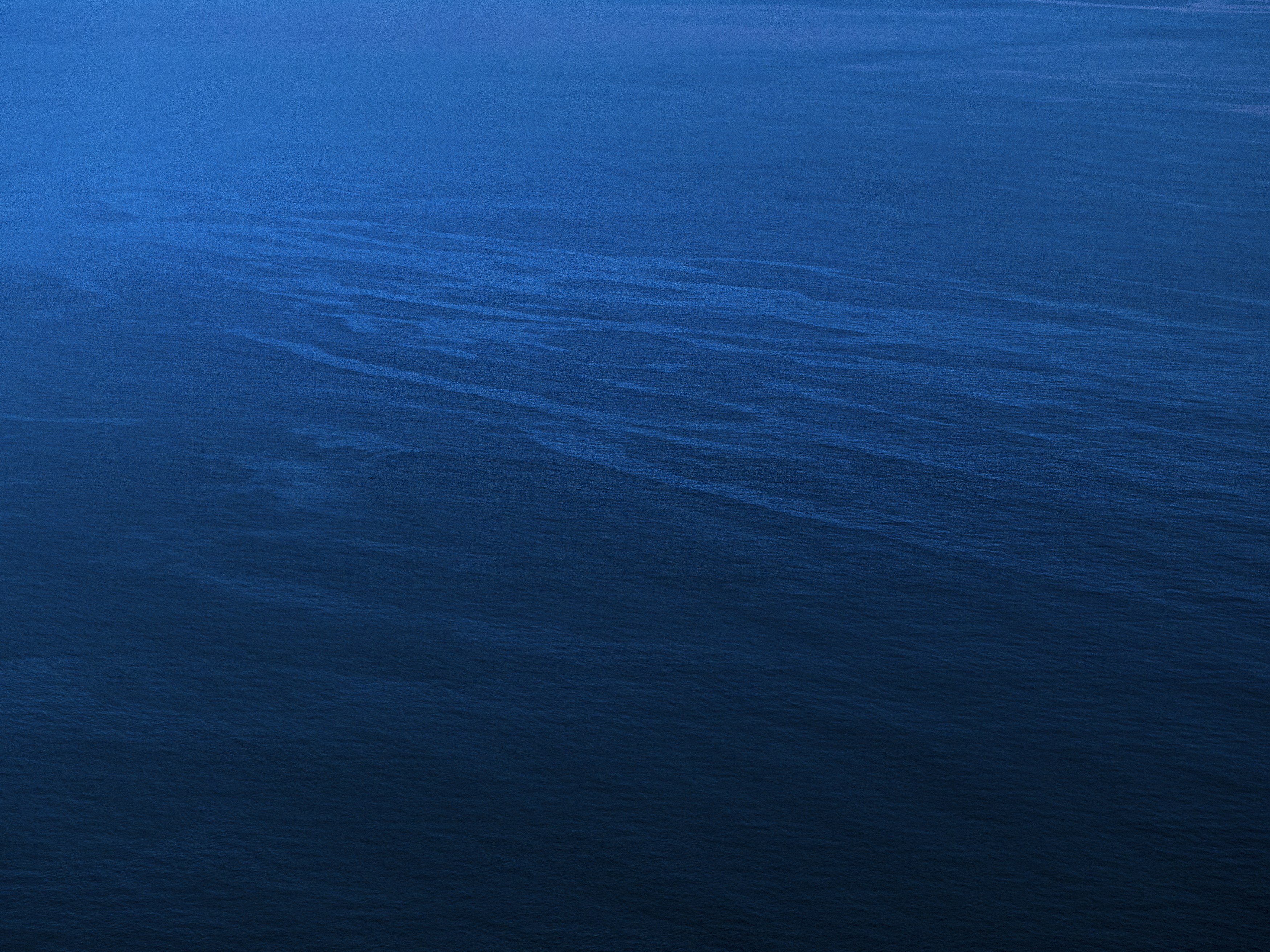 Gentle ocean waves create subtle patterns in deep blue water under soft lighting.