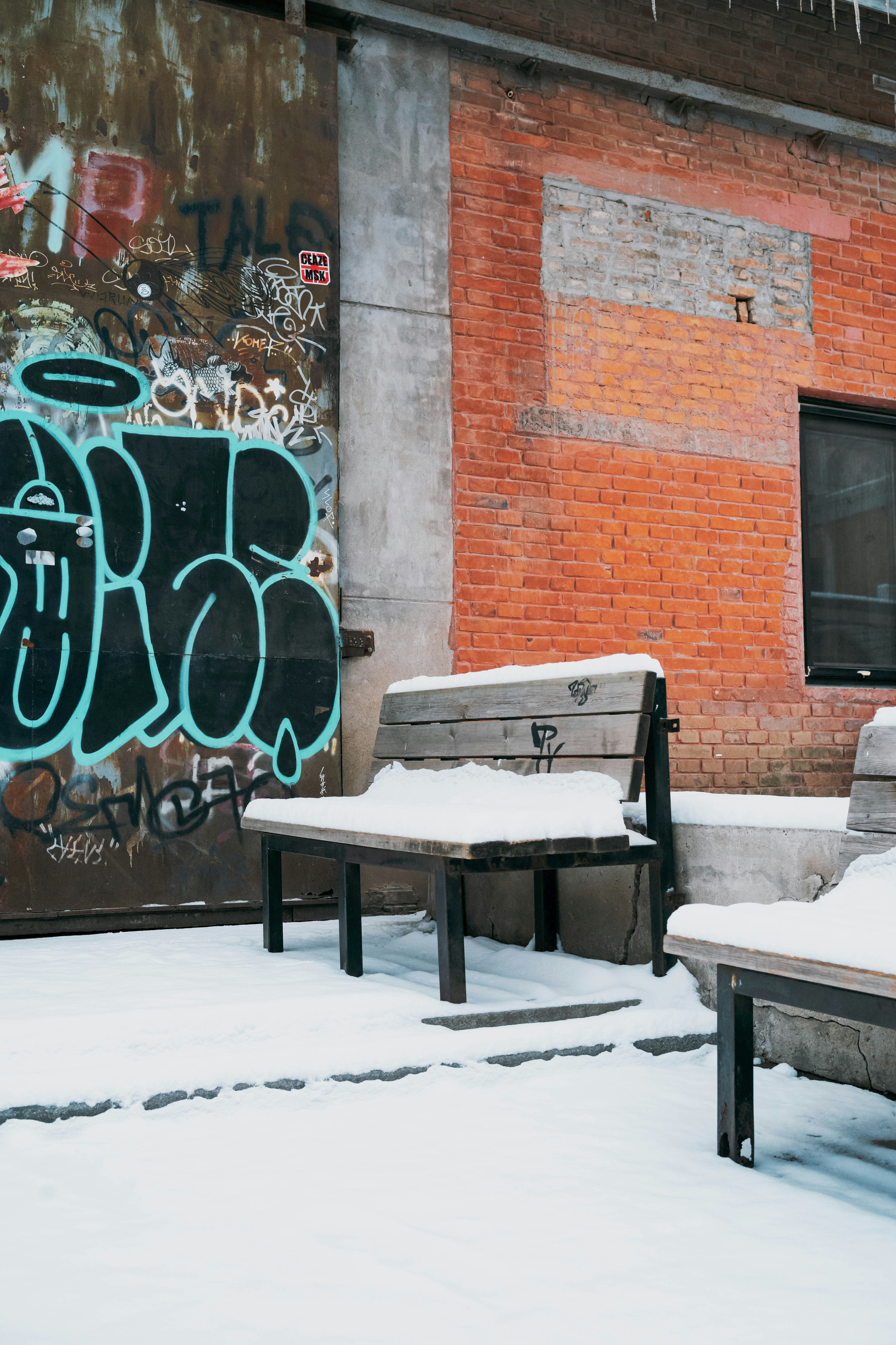 Snowy benches and graffiti against a brick wall