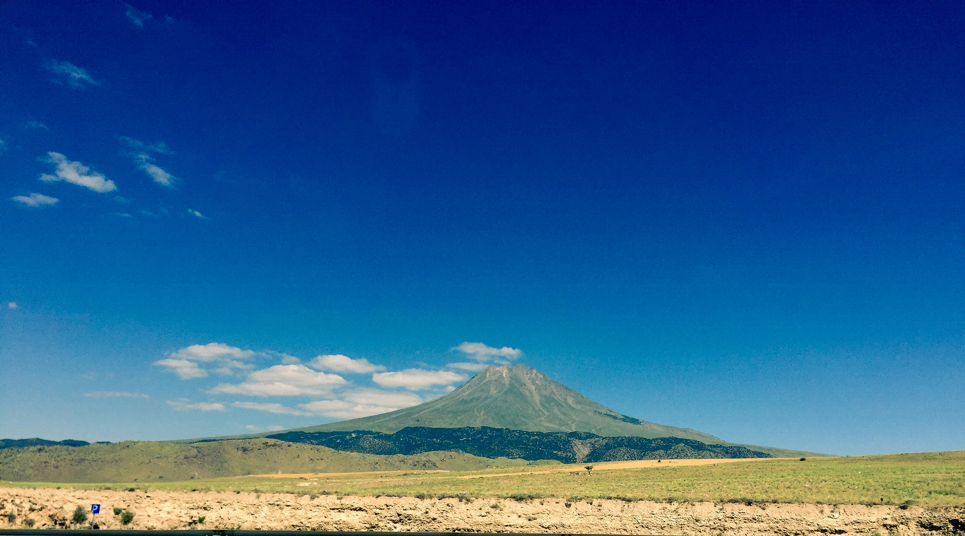 Distant mountain peak rising against a deep blue sky with scattered clouds.