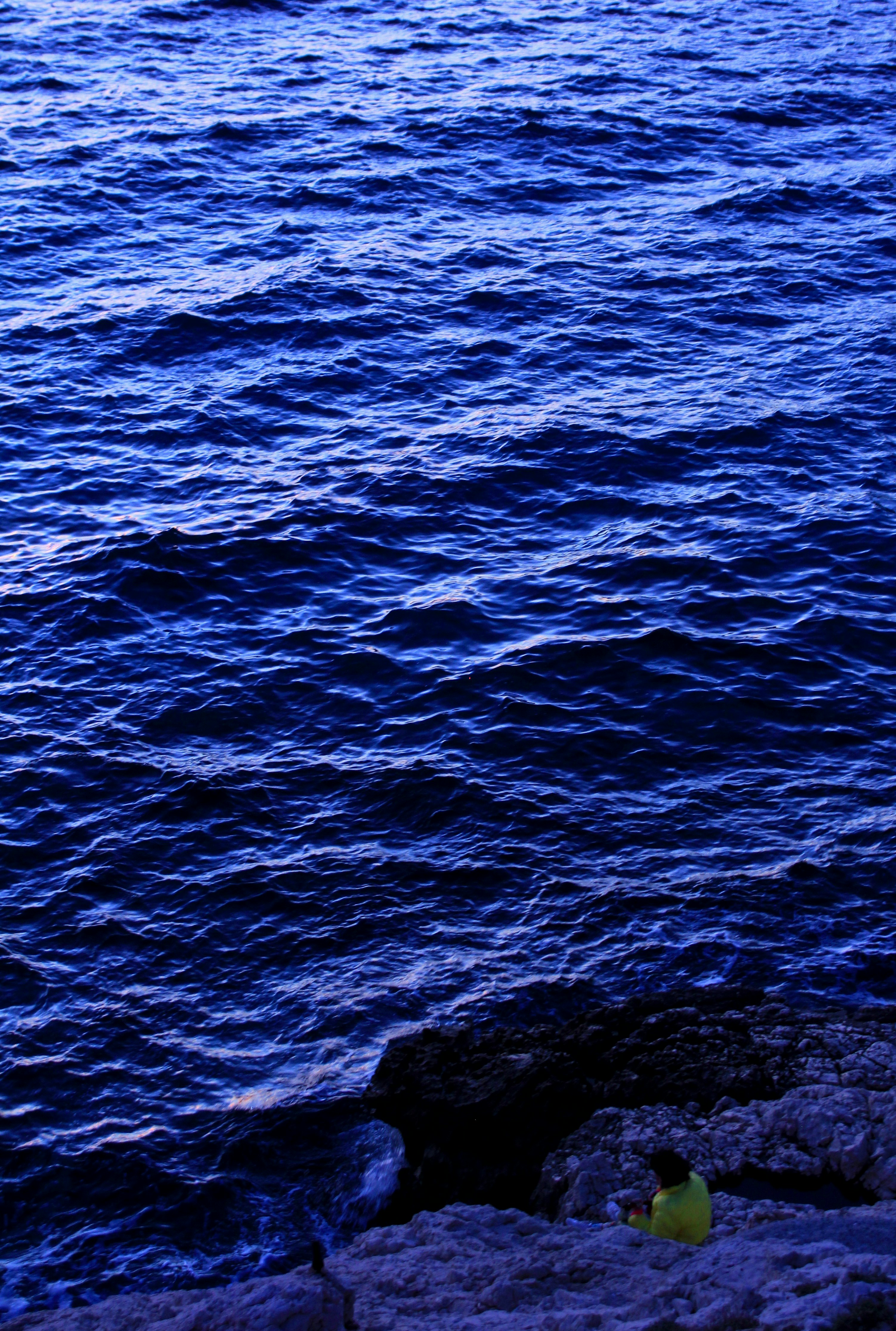 Azure Waves and a Lone Yellow Figure on the Rocky Edge