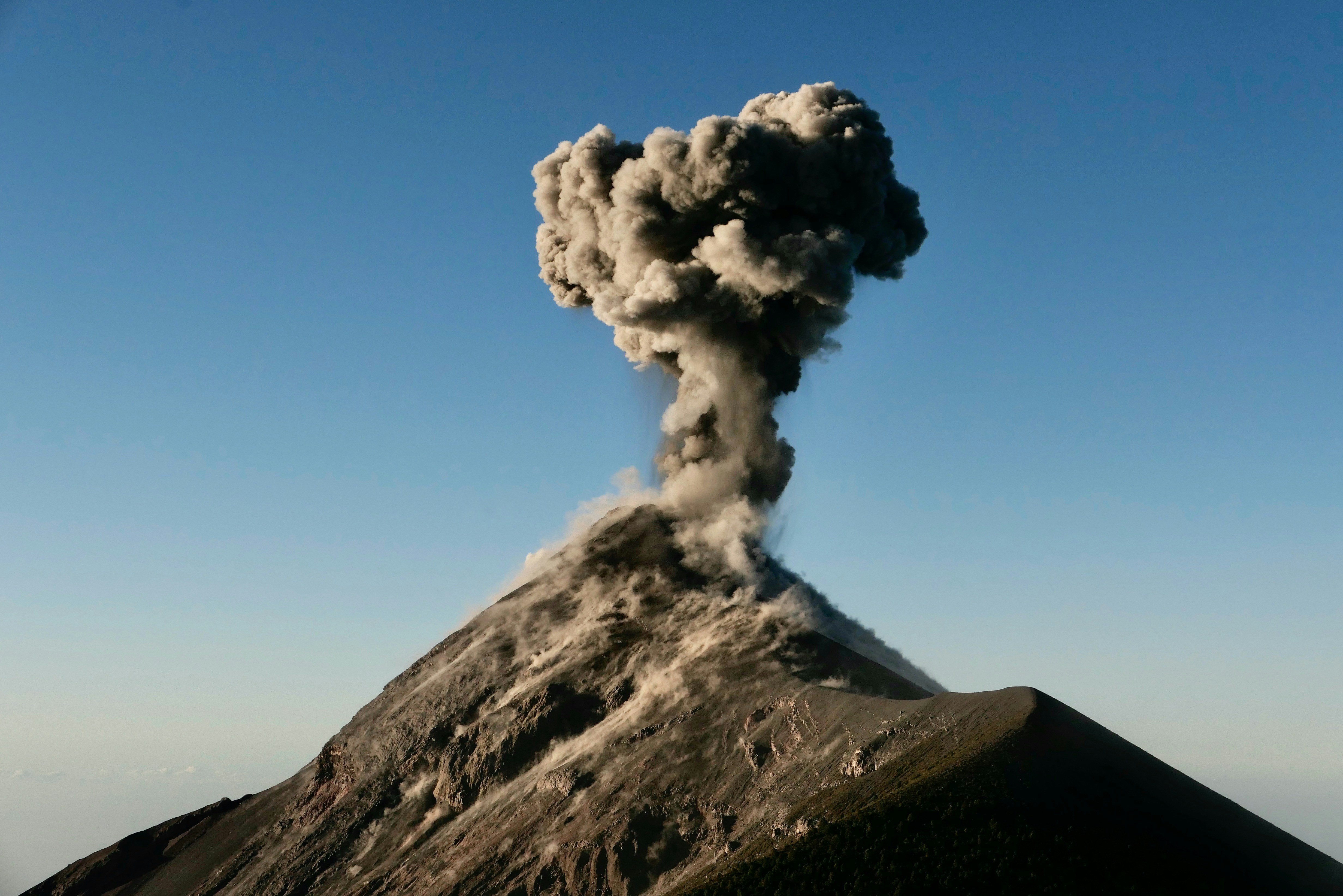 Volcano releasing a plume of ash and smoke under a clear blue sky.