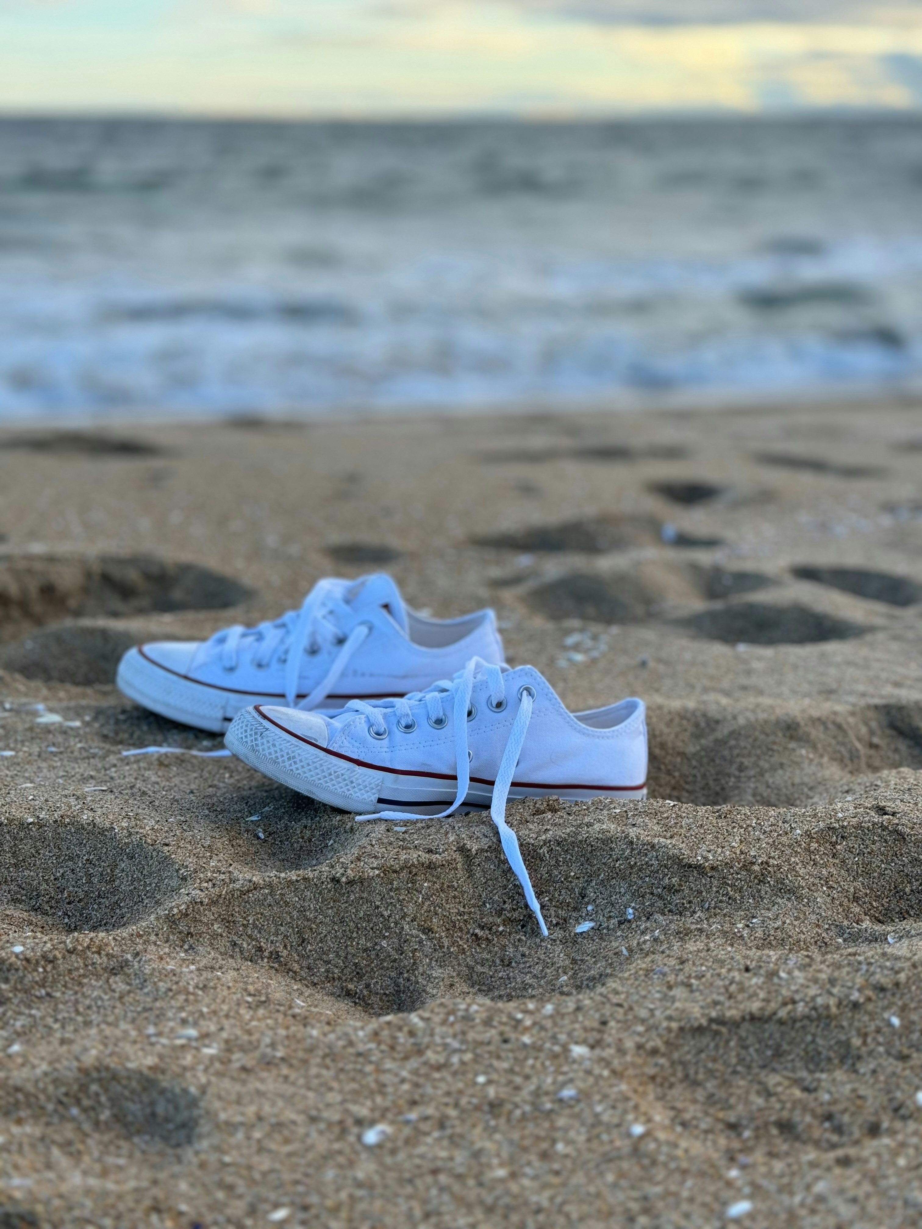 Two White Sneakers Rest on Wind-Touched Beach as Waves Blur in the Background