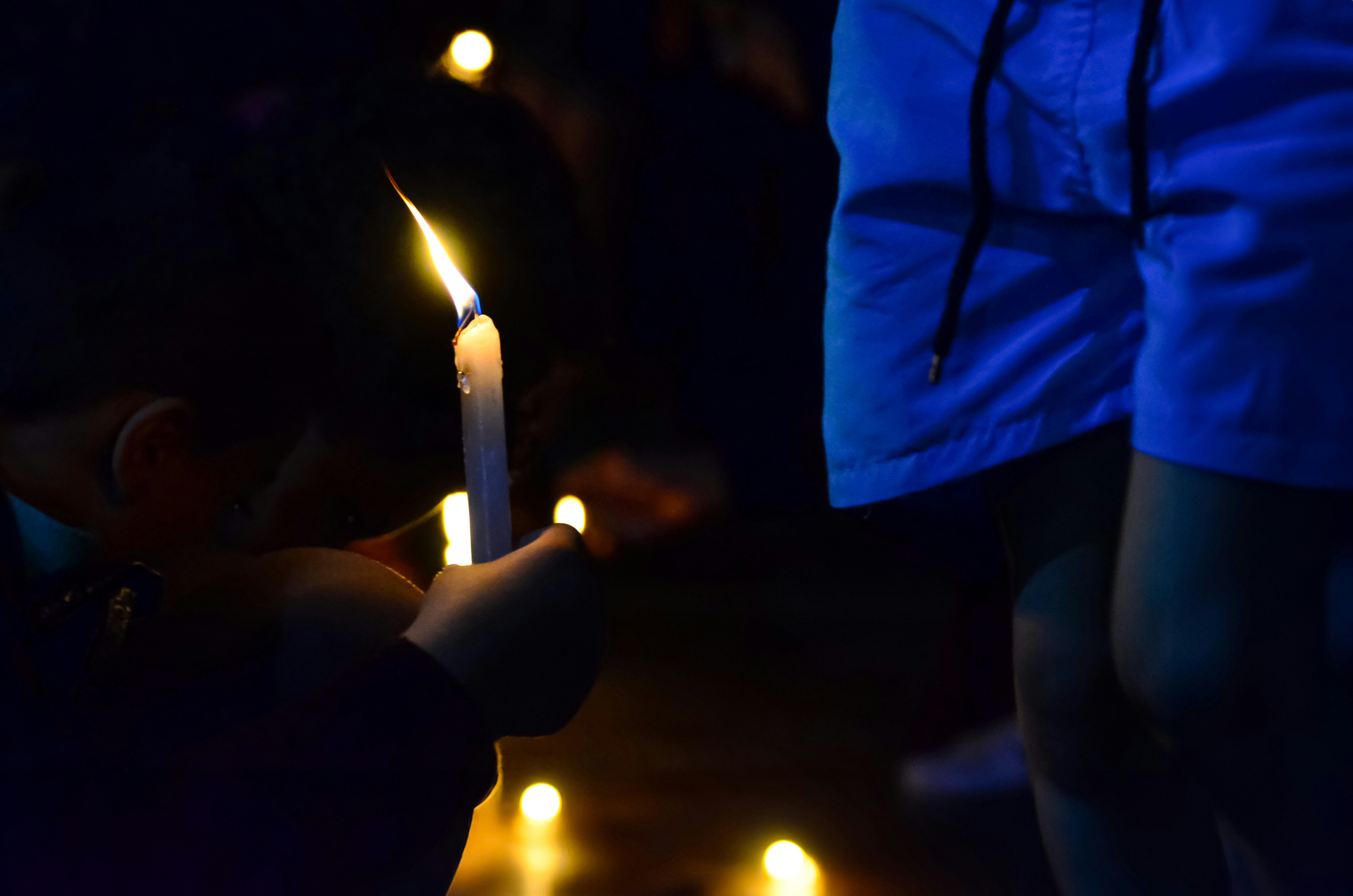 Person holding a lit candle in a dimly lit setting, with scattered candles on the floor creating a serene atmosphere.