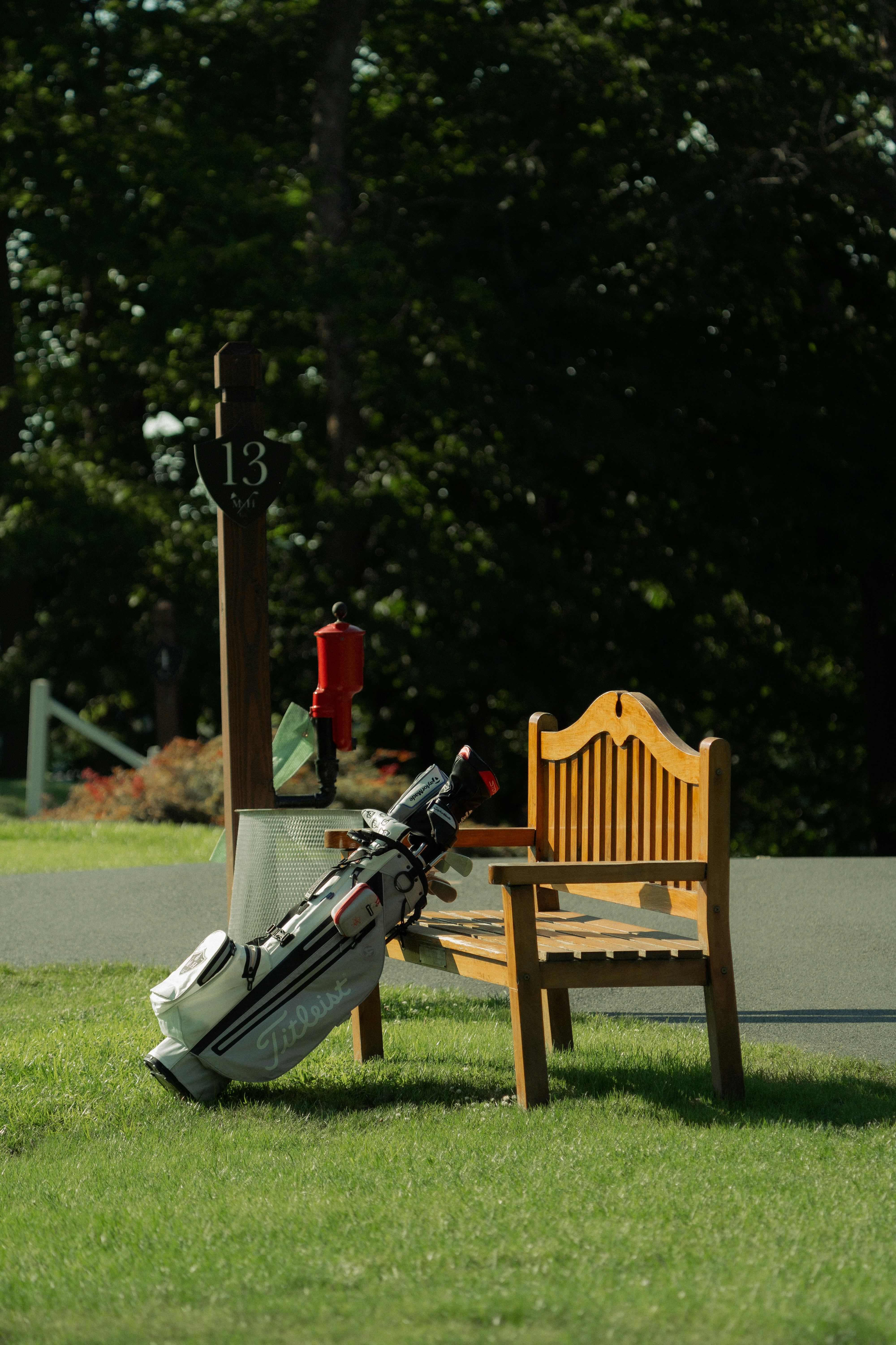 A wooden bench sitting in the grass next to a golf bag photo – Free ...