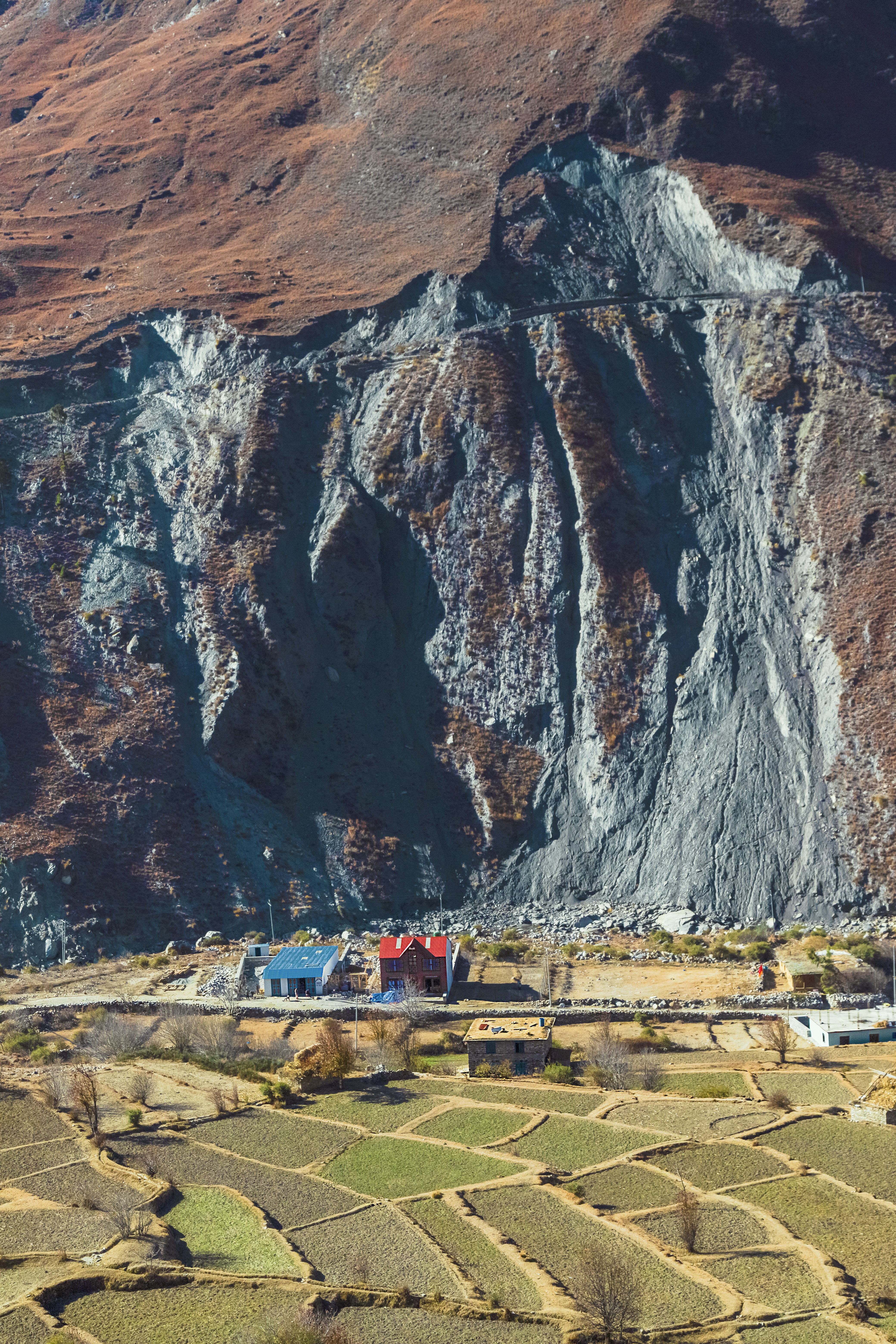 Red-roofed cottage anchors a terraced valley beneath a towering cliff