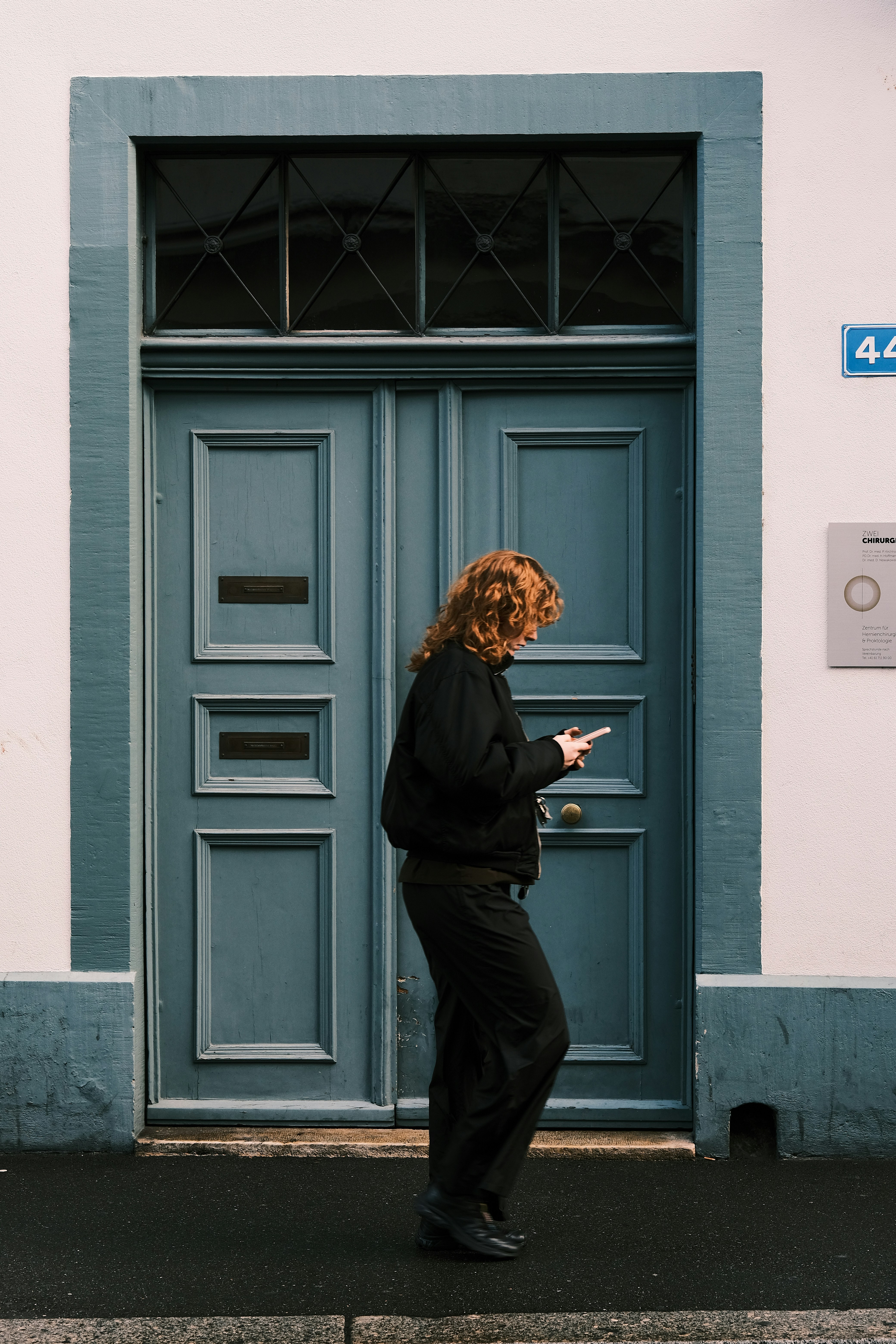 Blue Doorway Stroll: A Woman in Black Pauses with a Phone