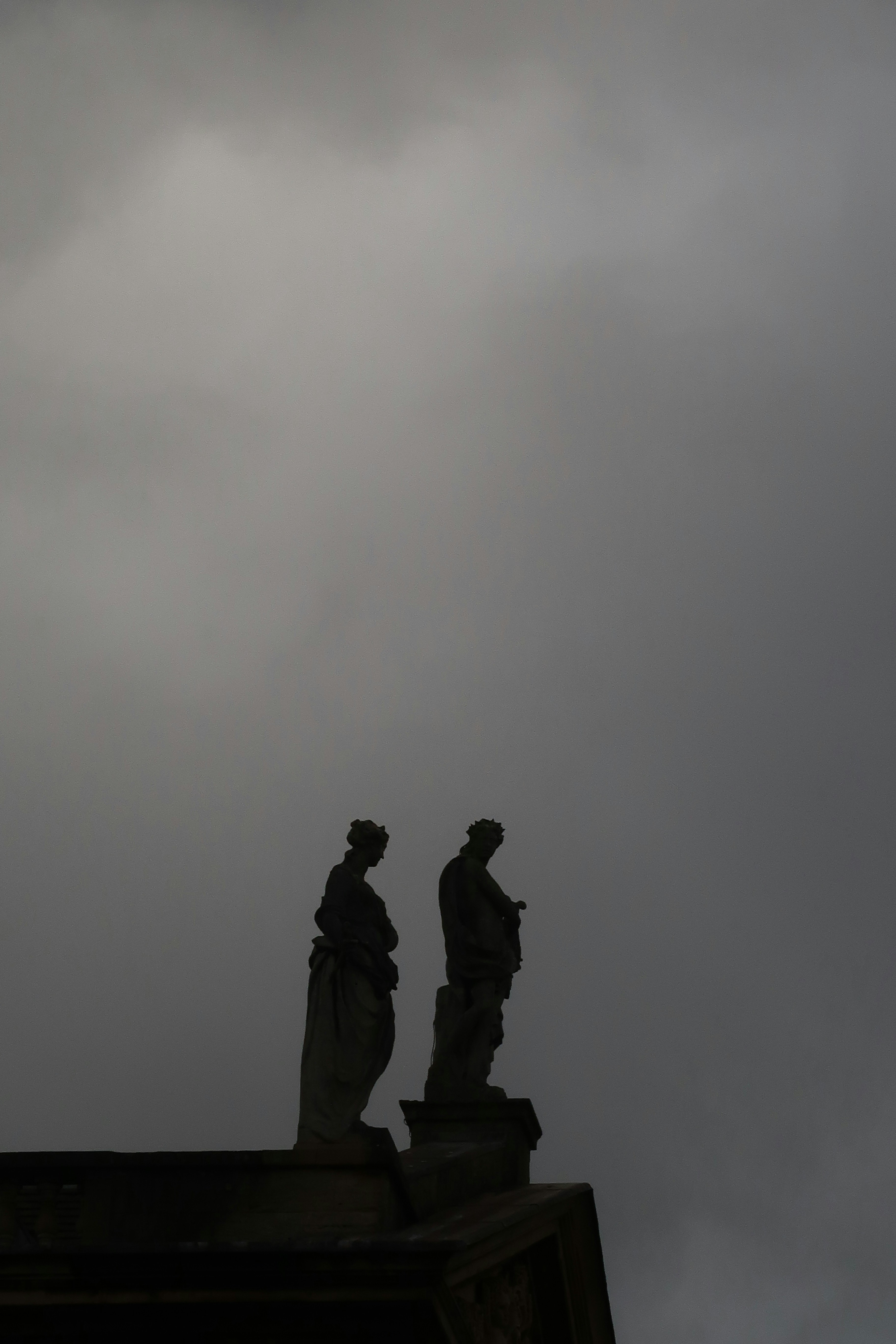 Two statues stand atop a building under a dark, cloudy sky.