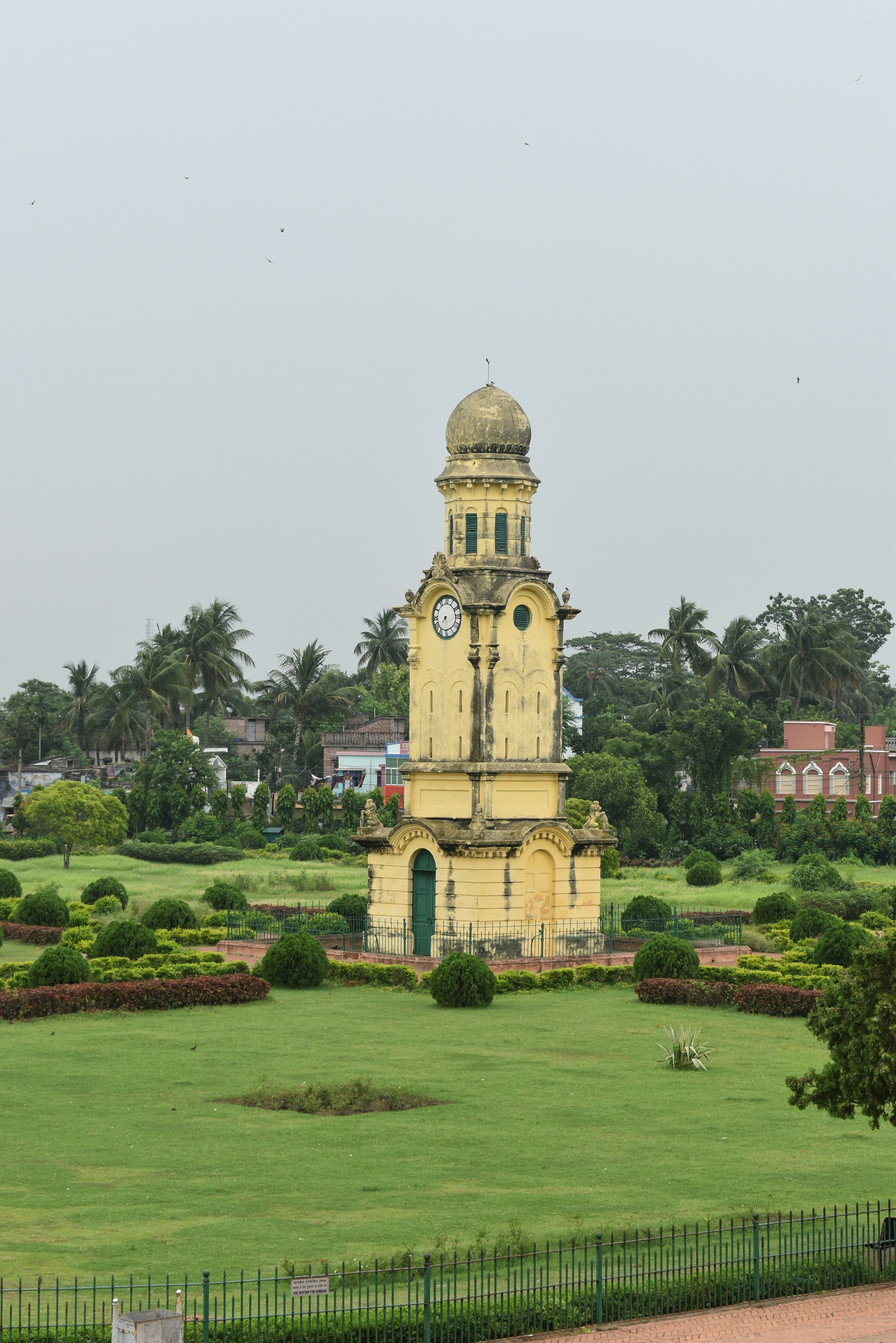A large yellow clock tower sitting in the middle of a lush green field ...