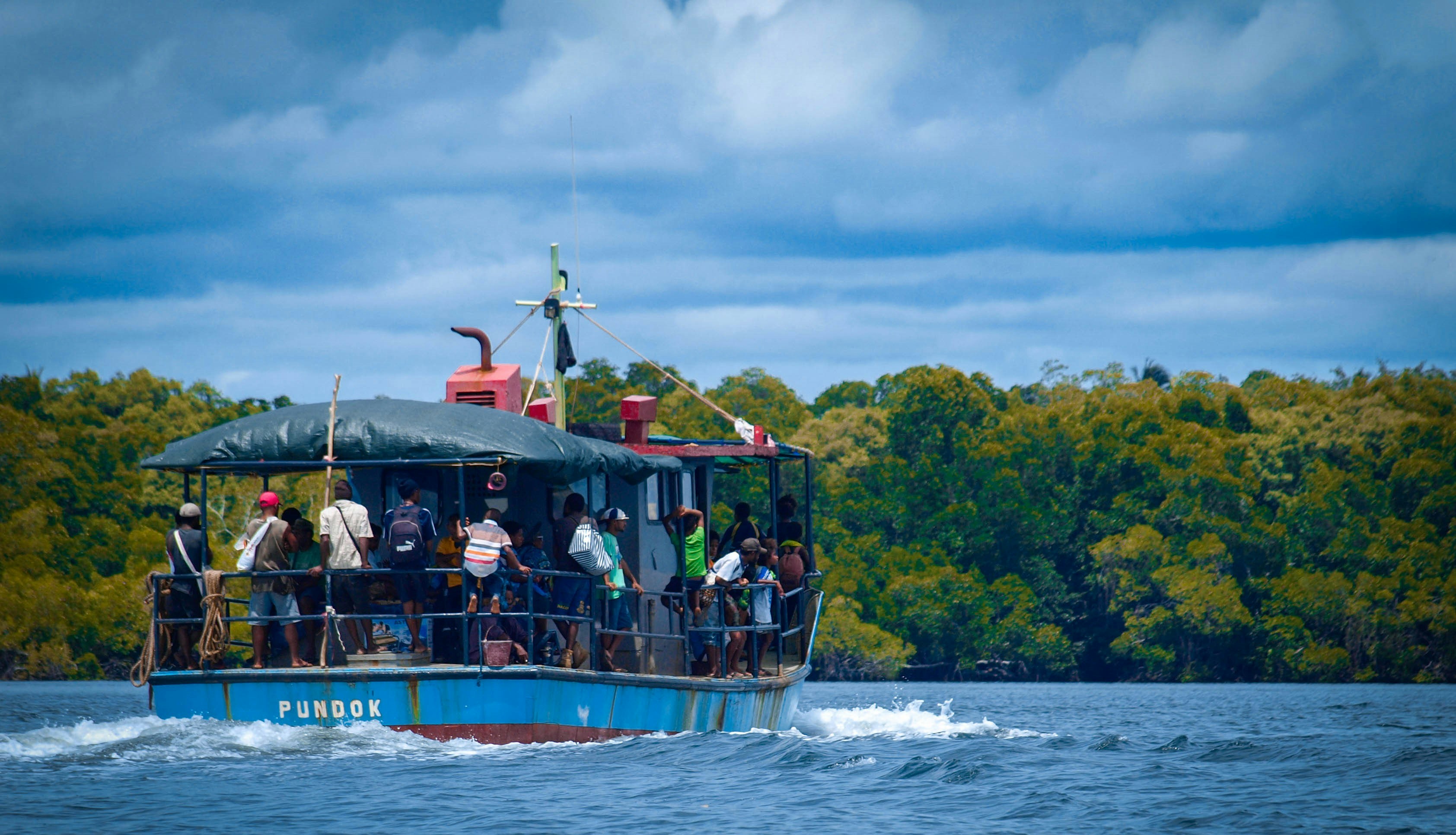 A boat carrying passengers glides across a lake with dense forest in the background and dramatic cloud cover overhead.