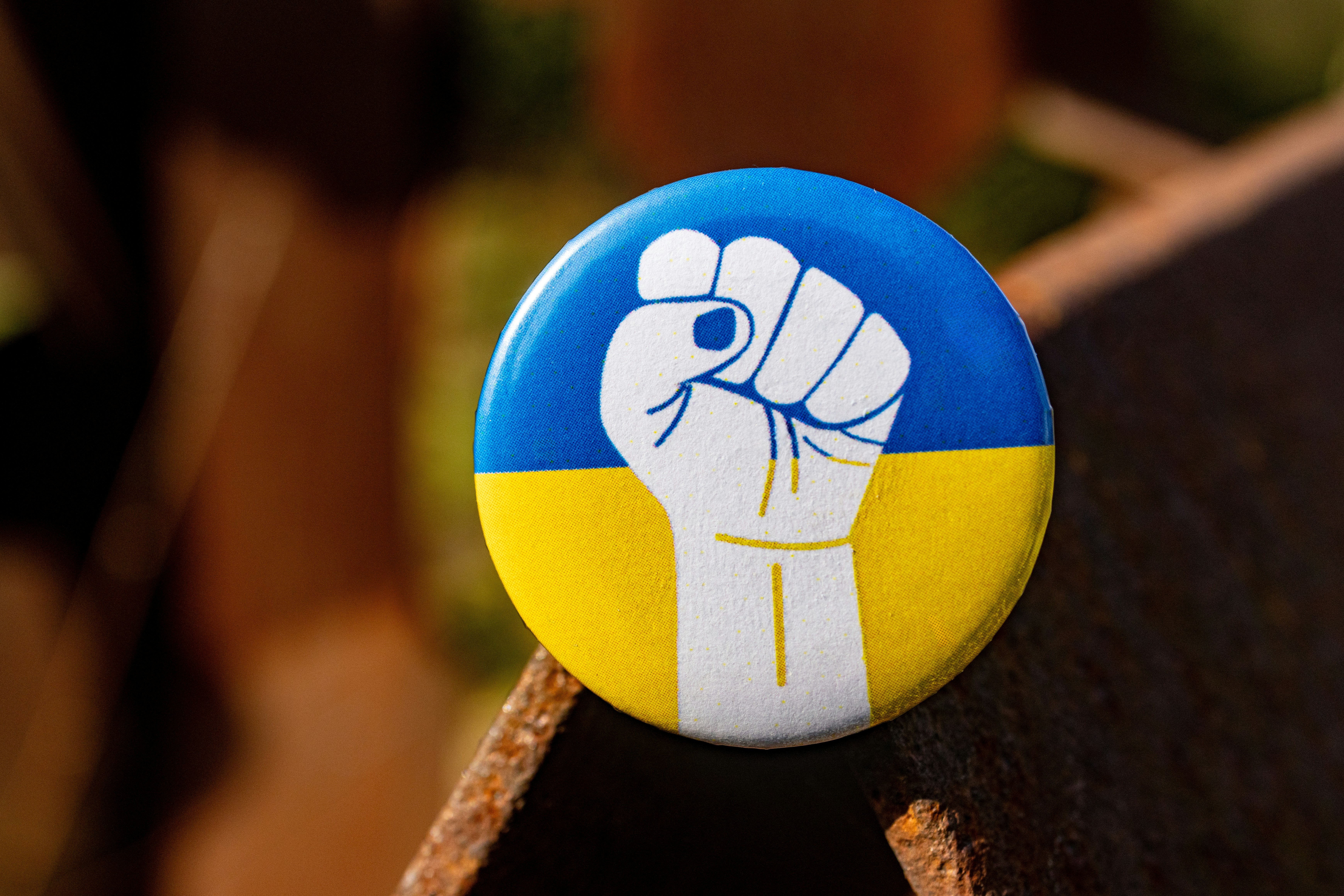 Enamel badge of a raised fist in blue and yellow on a weathered rail
