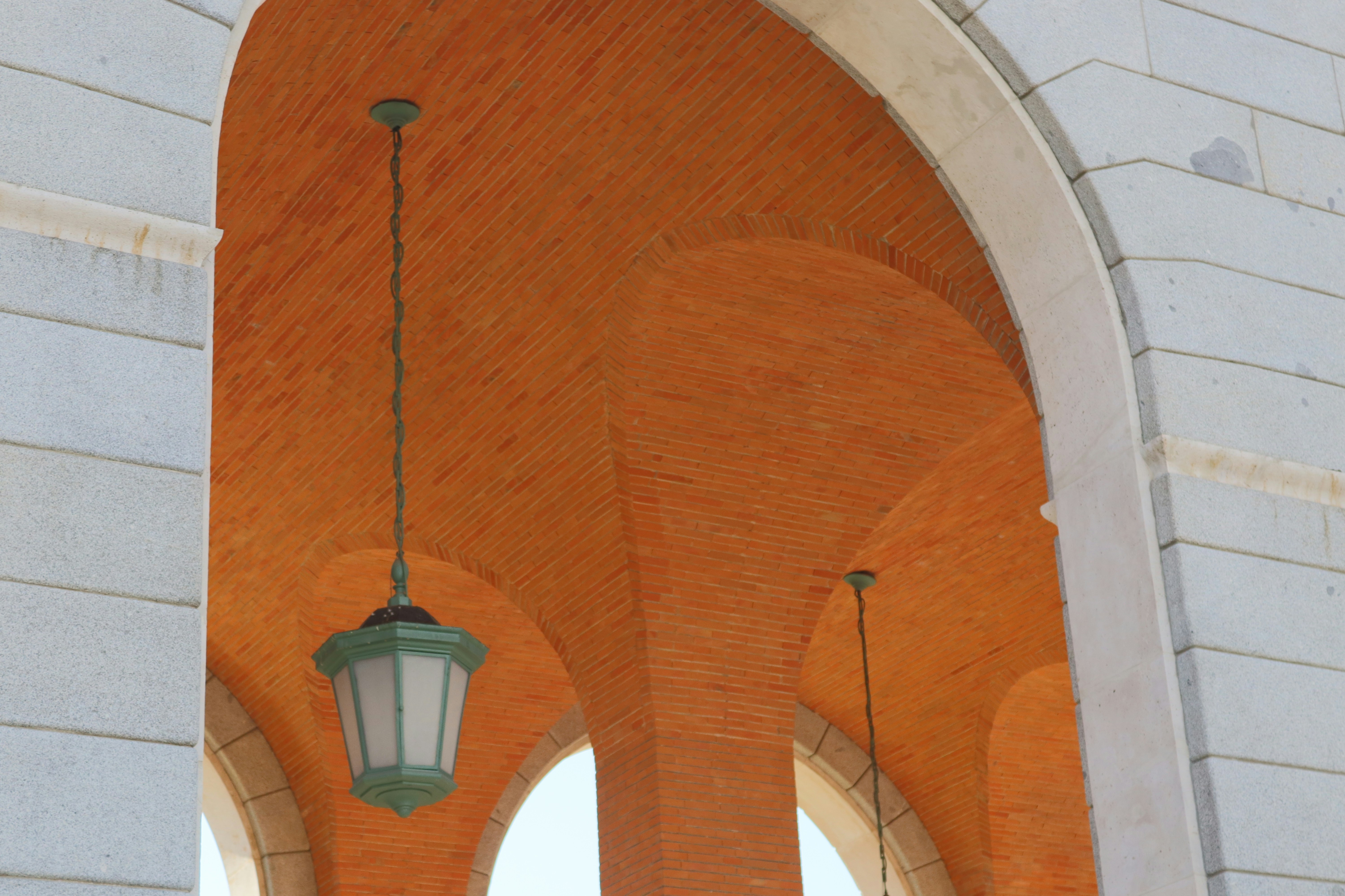 Between Brick Arches: Lanterns Hover Over a Sunlit Arcade