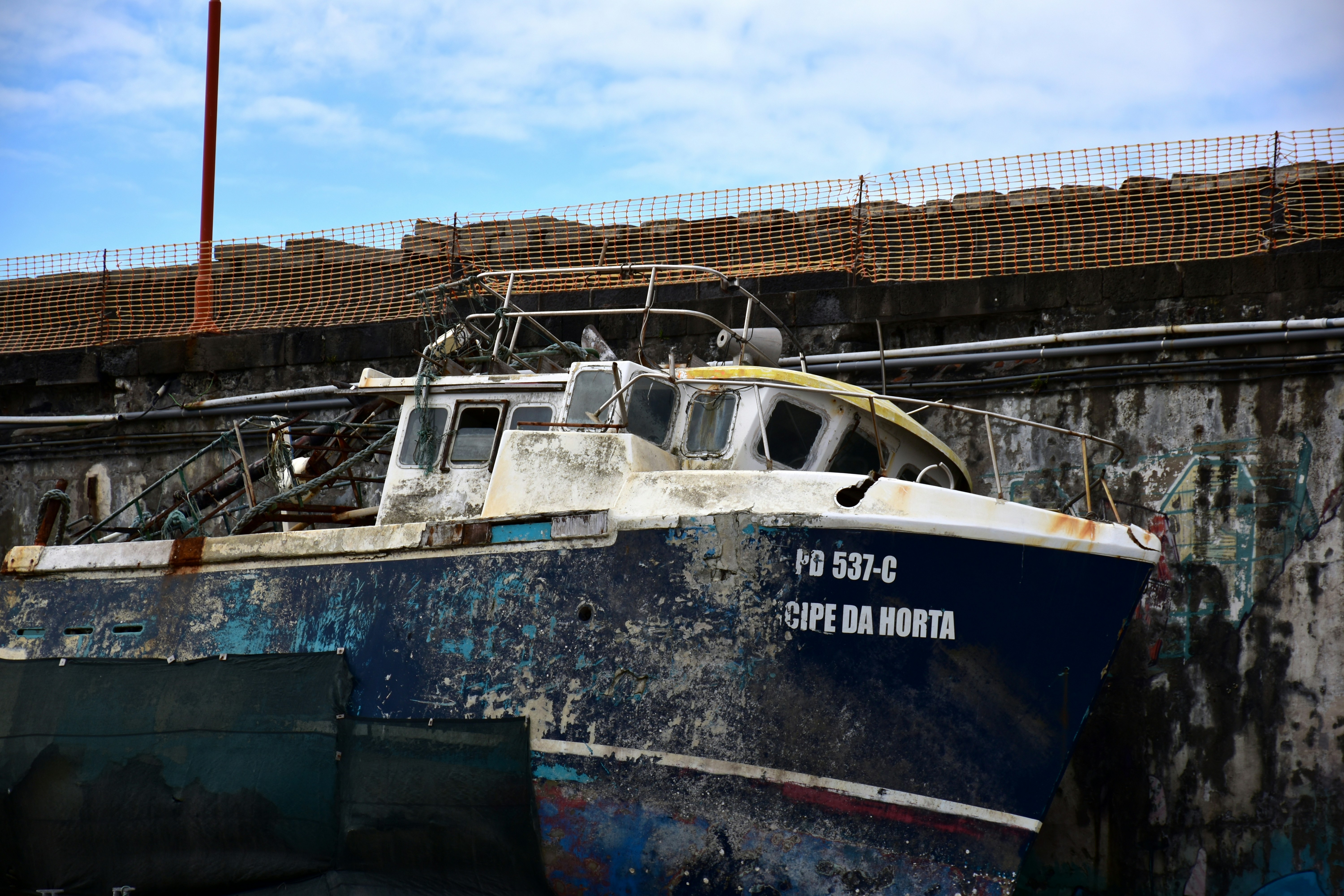 Weathered fishing boat rests against a dilapidated harbor wall, showcasing the passage of time and neglect.