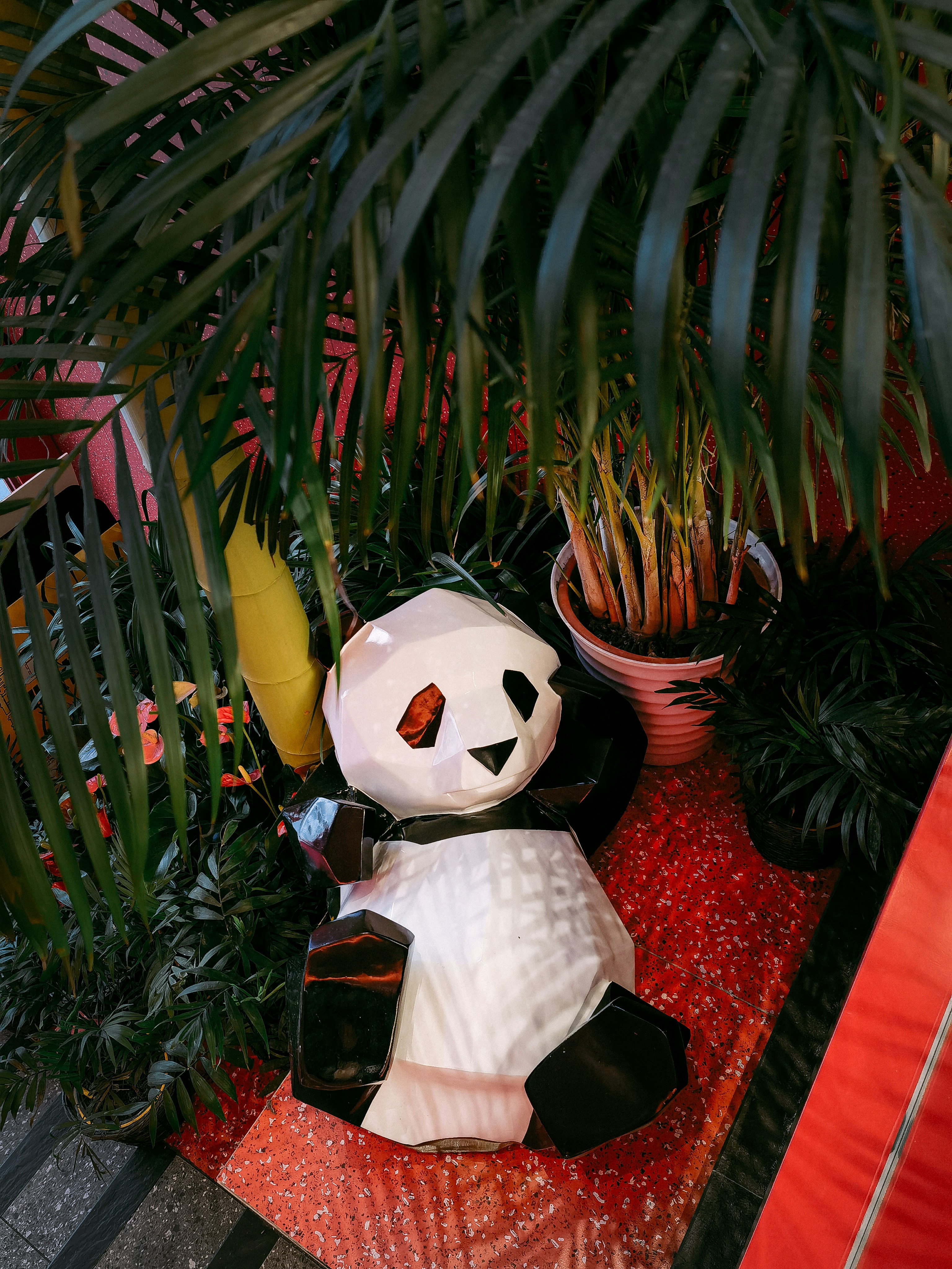Geometric Panda Among Tropical Greens: A Quiet Indoor Sculpture on Red Terrazzo