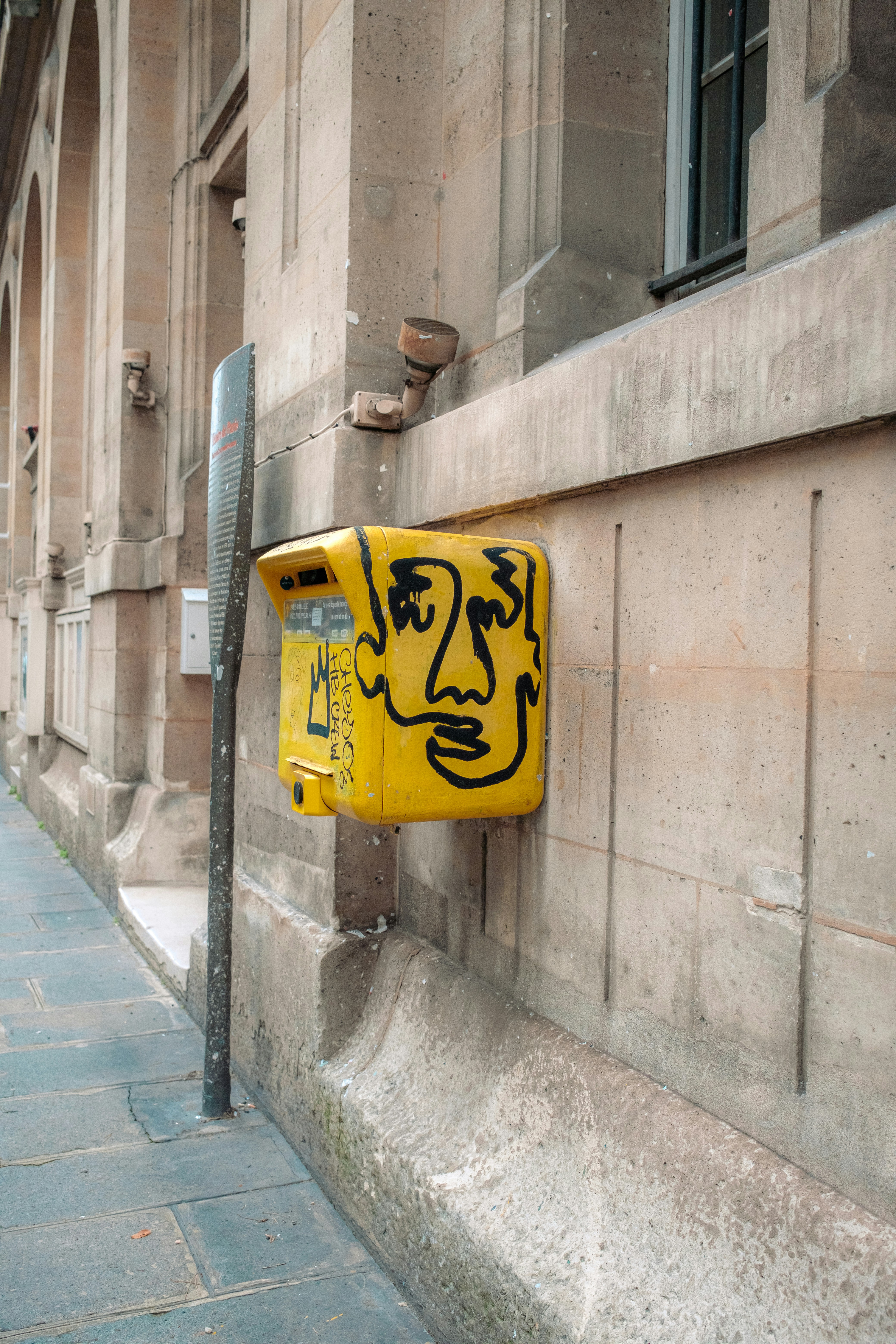 Urban Post: The Yellow Mailbox with Graphical Face on a Stone Wall