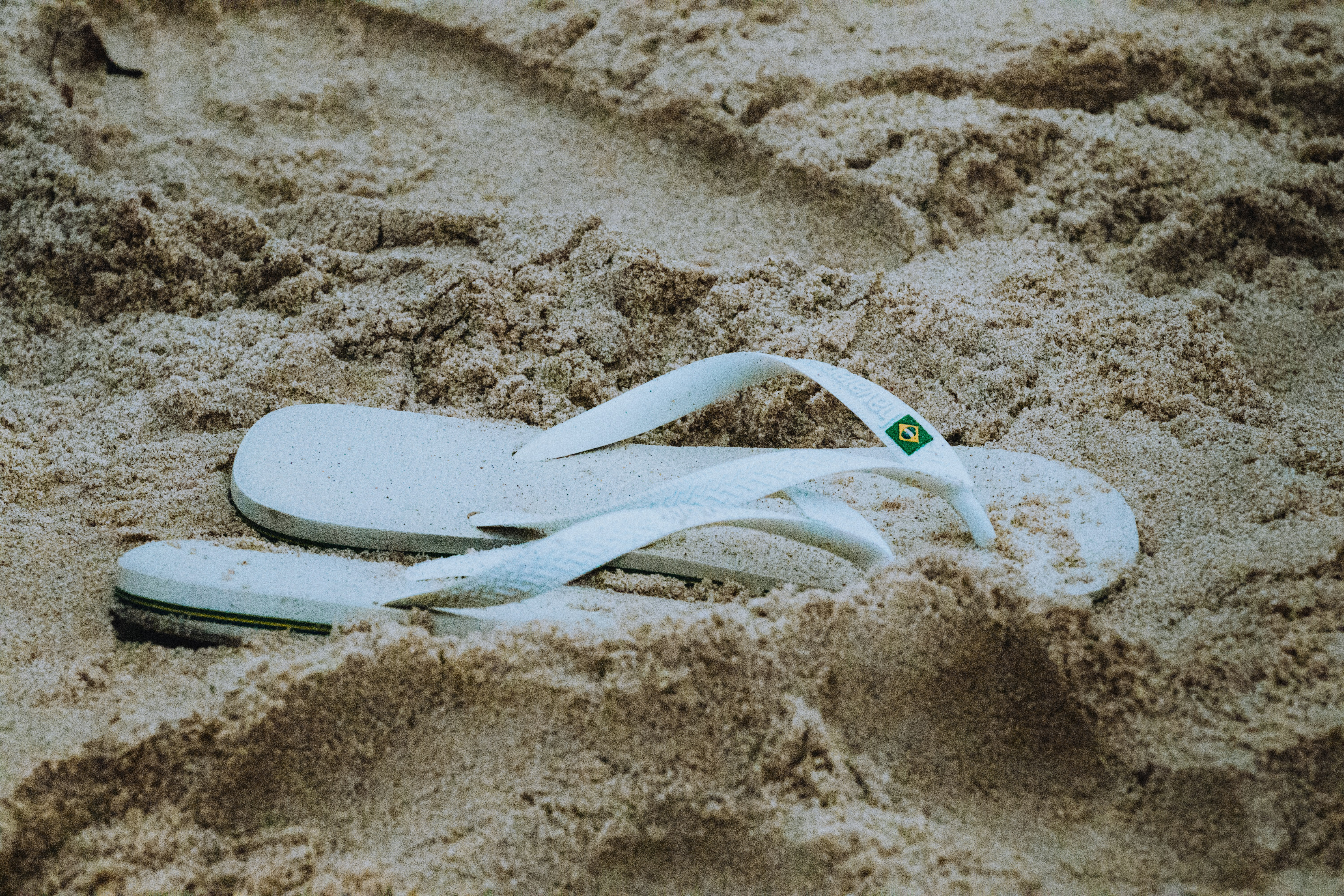 White flip flops nestled in textured sandy beach.