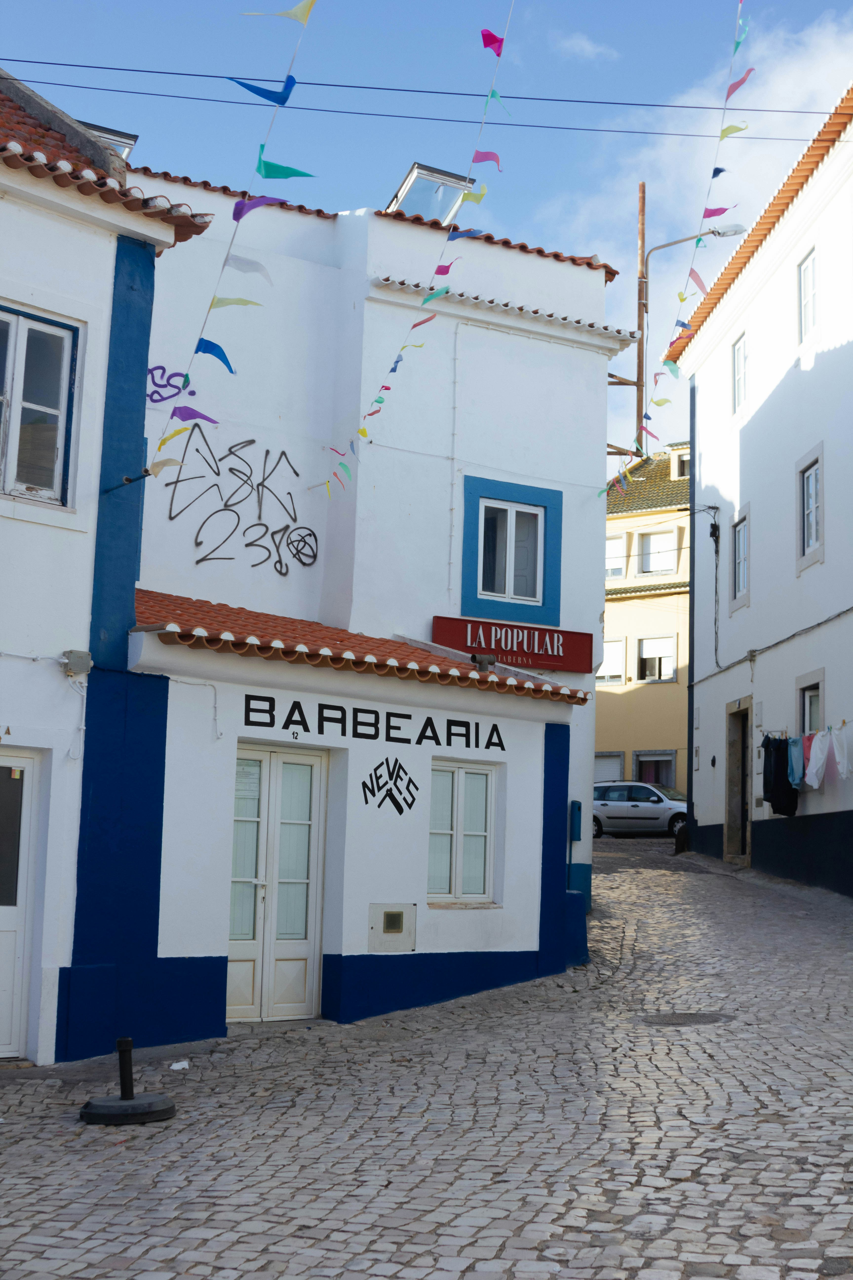 Barbearia on a sunlit cobblestone lane under festive pennants