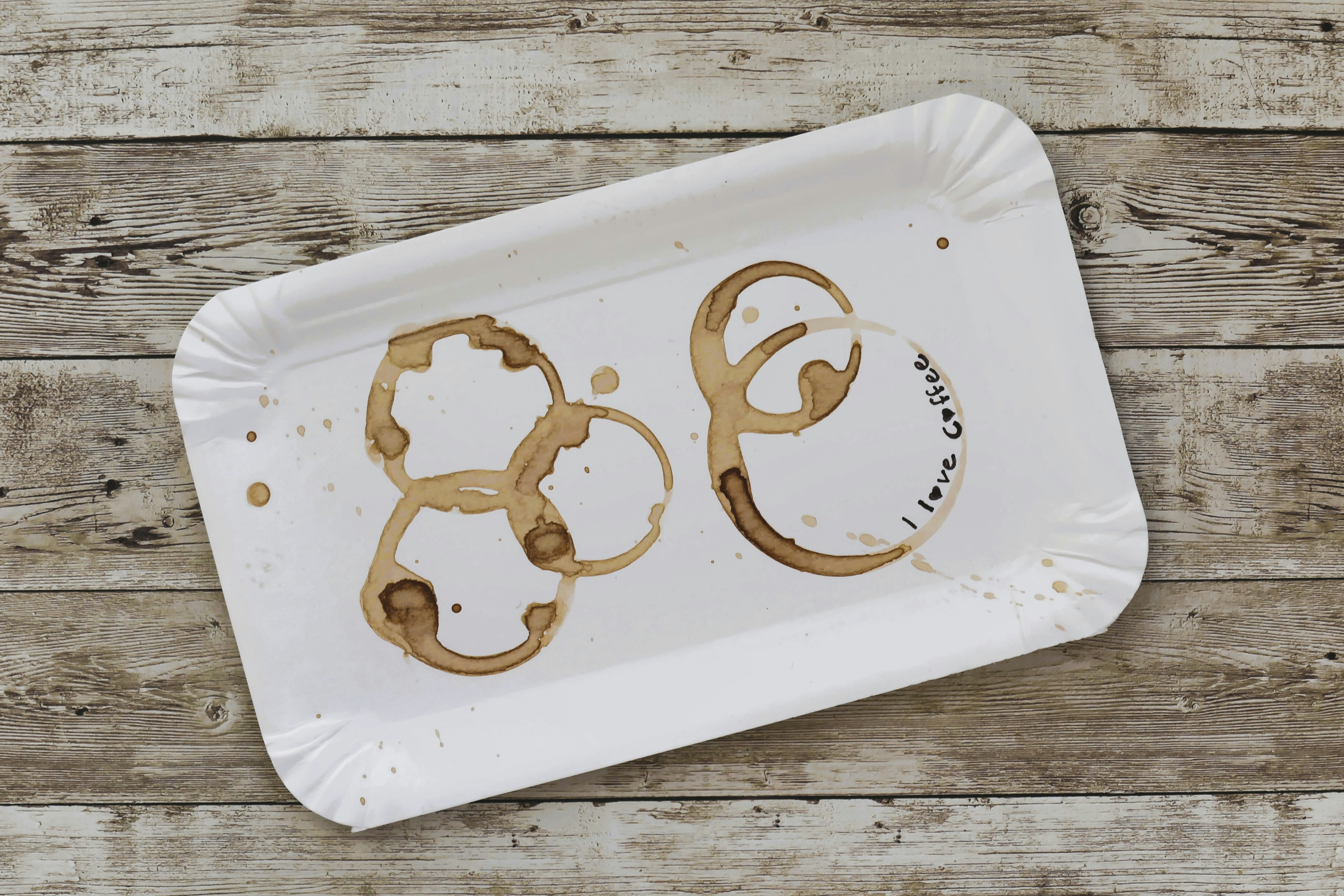 Coffee stains form patterns on a white paper tray placed on a wooden surface.