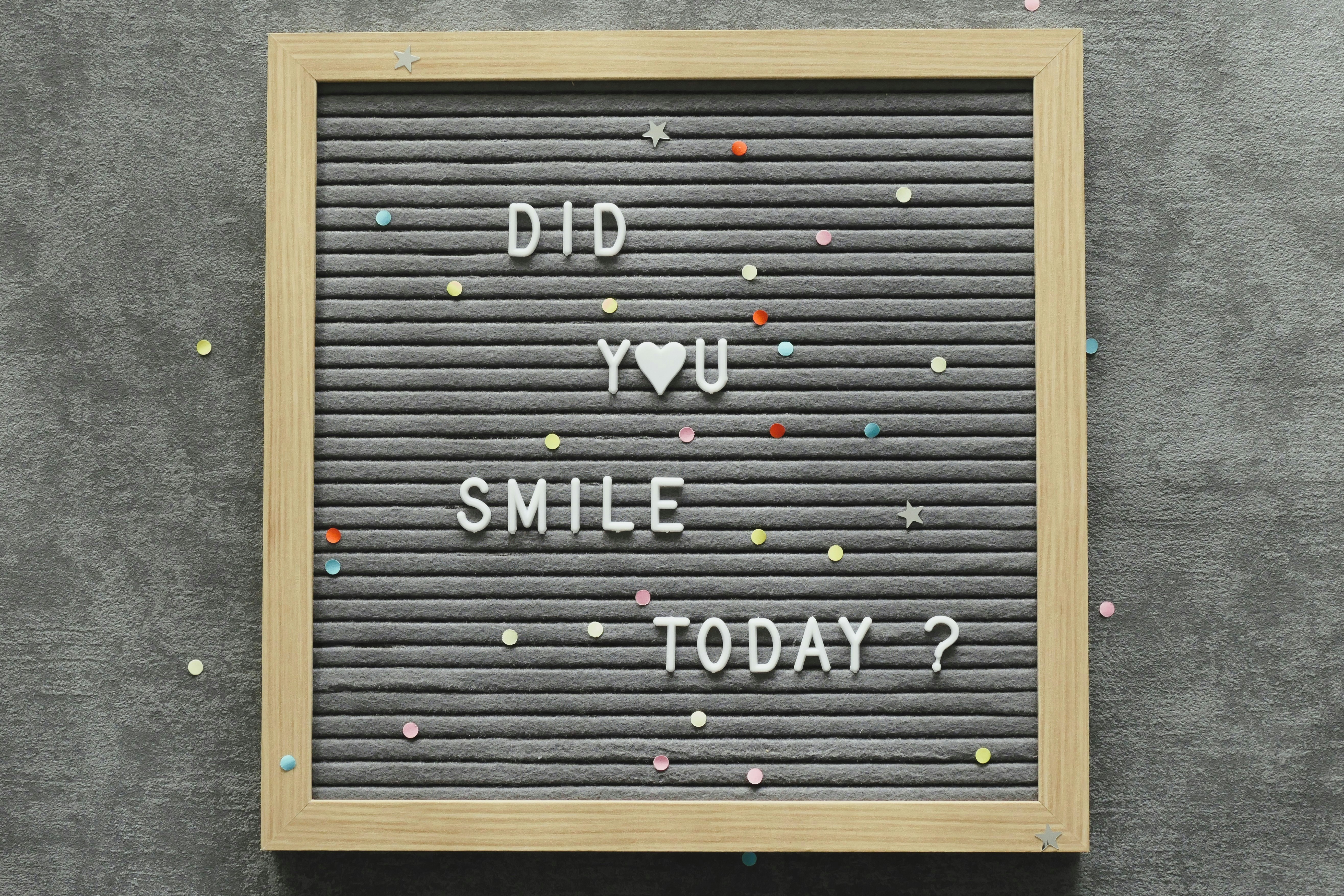 Letter board with the phrase 'DID YOU SMILE TODAY?' surrounded by colorful confetti-like dots. The letters are set against a textured gray background.