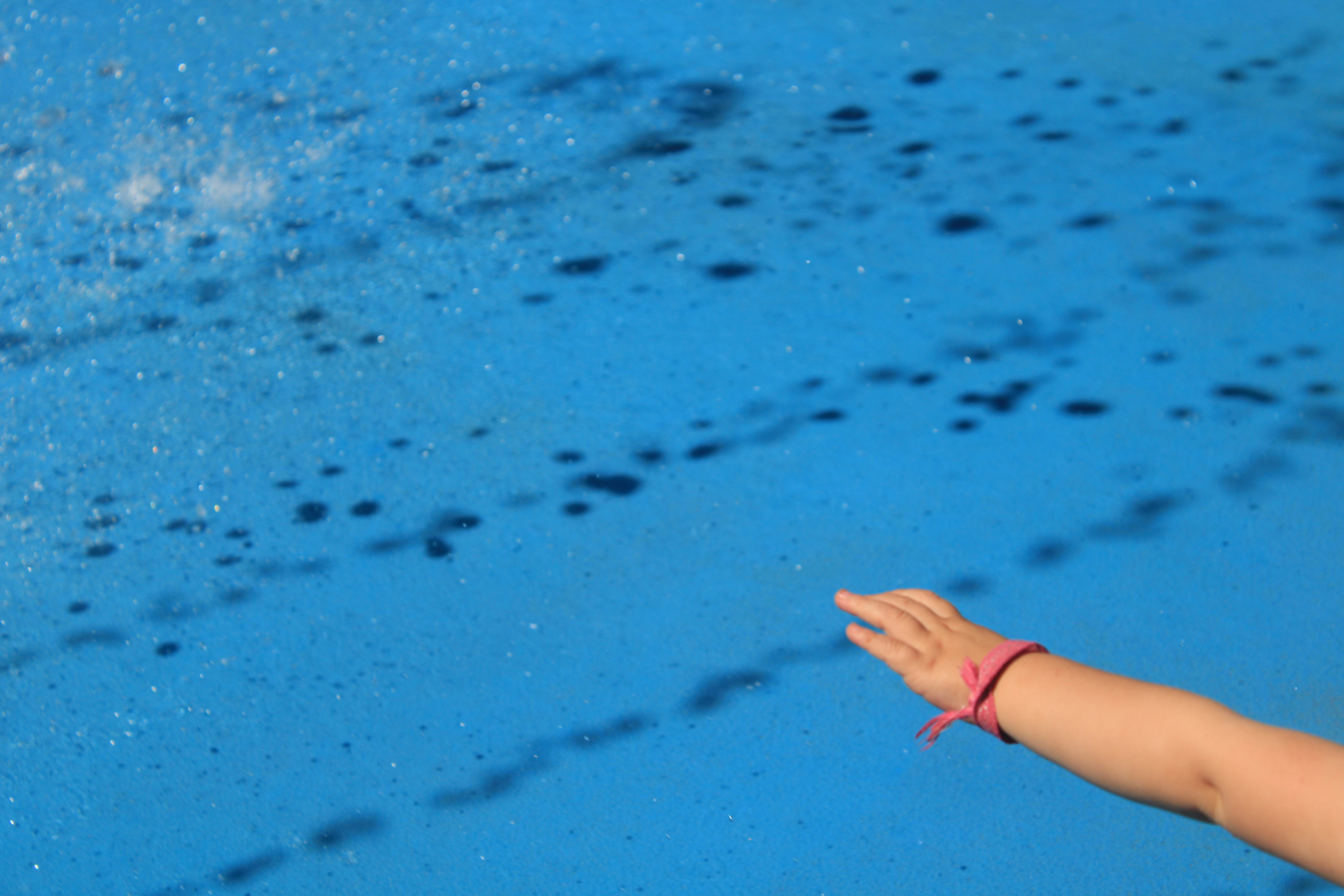 Arm Reaches Toward a Sparkling Blue Pool as Water Droplets Scatter