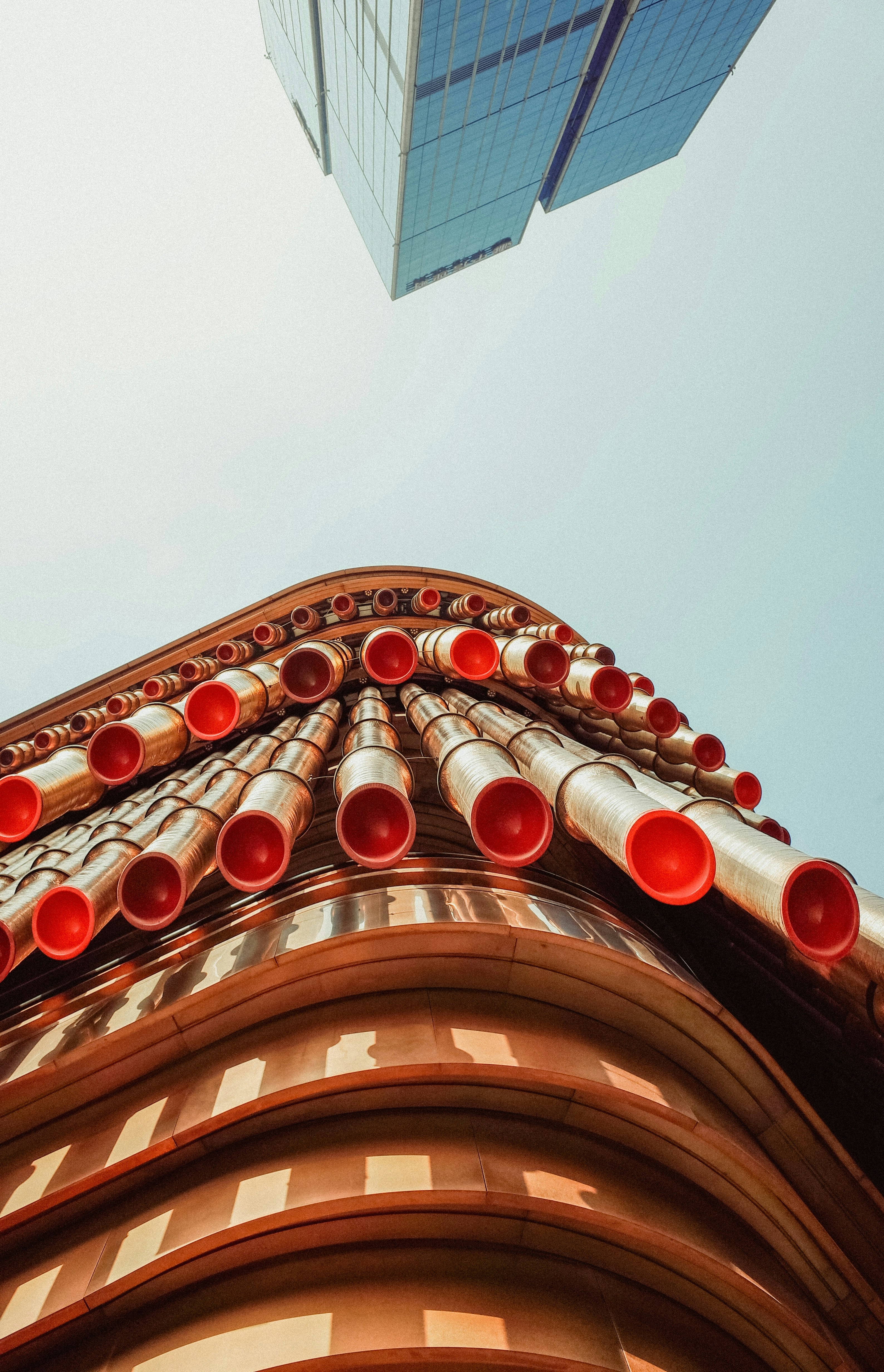 Urban Crown: A Ribbon of Red Tubes Arching along a Curved Facade Beneath a Towering Sky