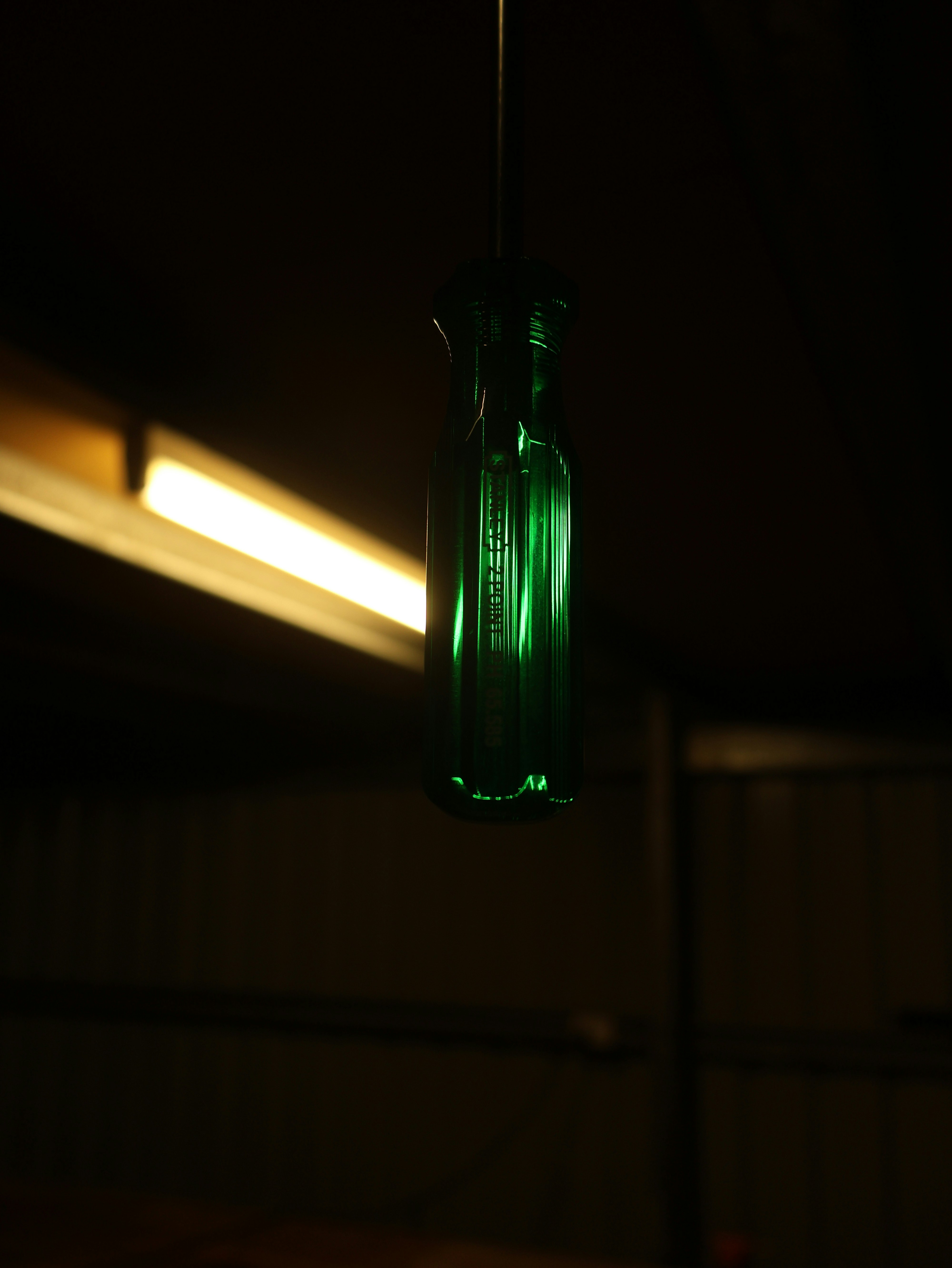 Emerald Pendant: A Green Bottle Suspended in Dim Warehouse Glow