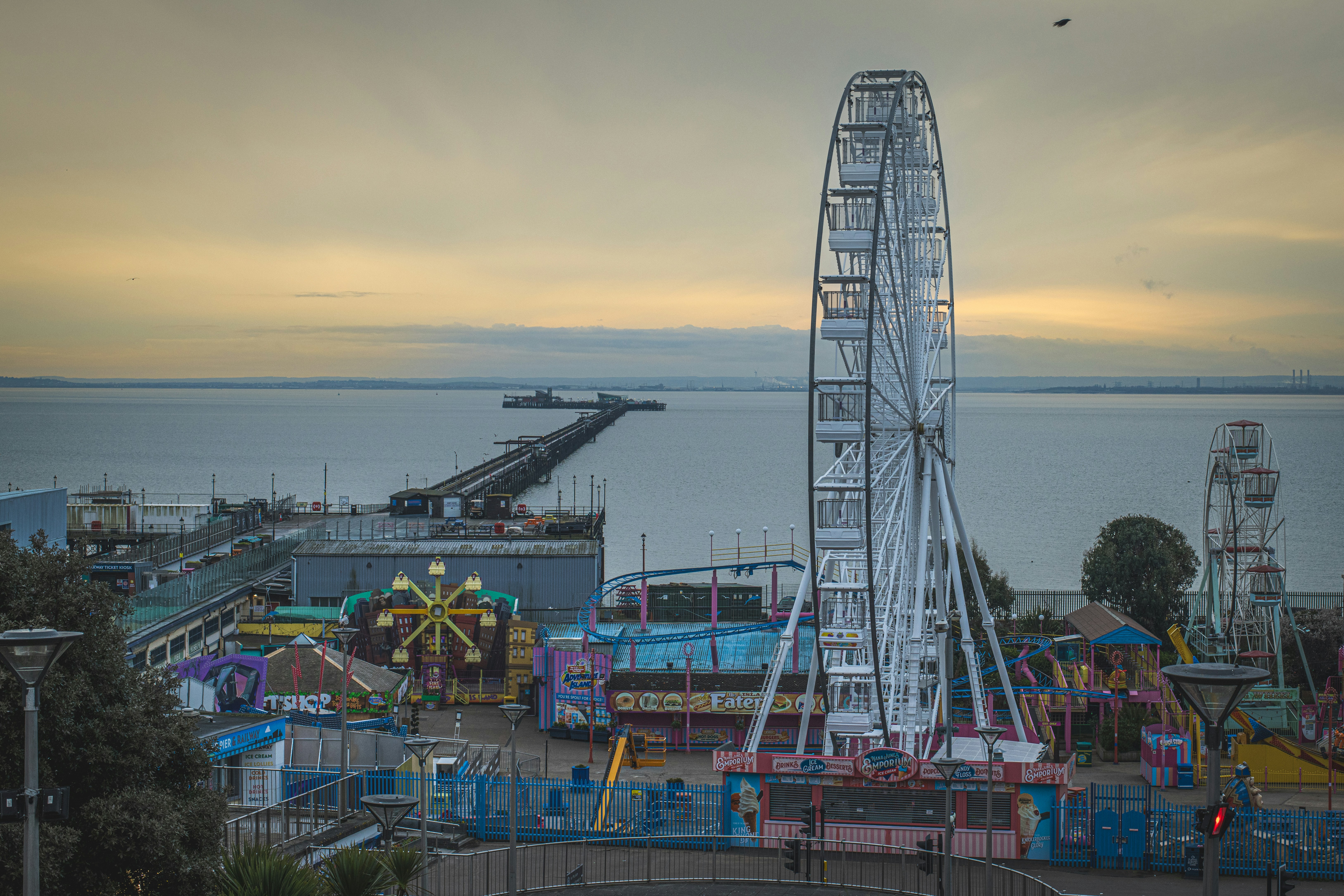 Ferris wheel overlooking a seaside pier at sunset with a moody sky.
