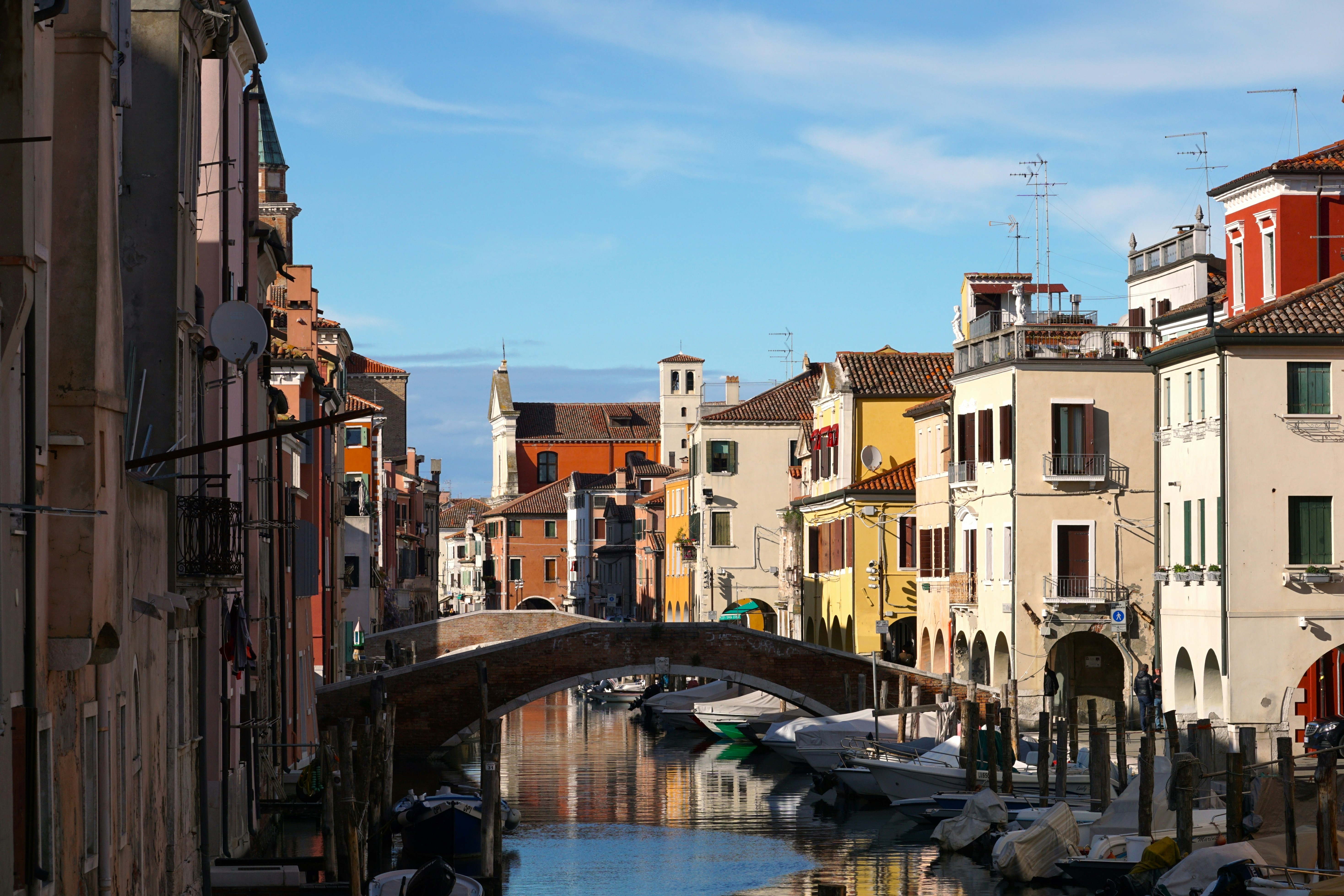 Quaint bridge arches over a narrow canal flanked by colorful buildings under a clear blue sky.